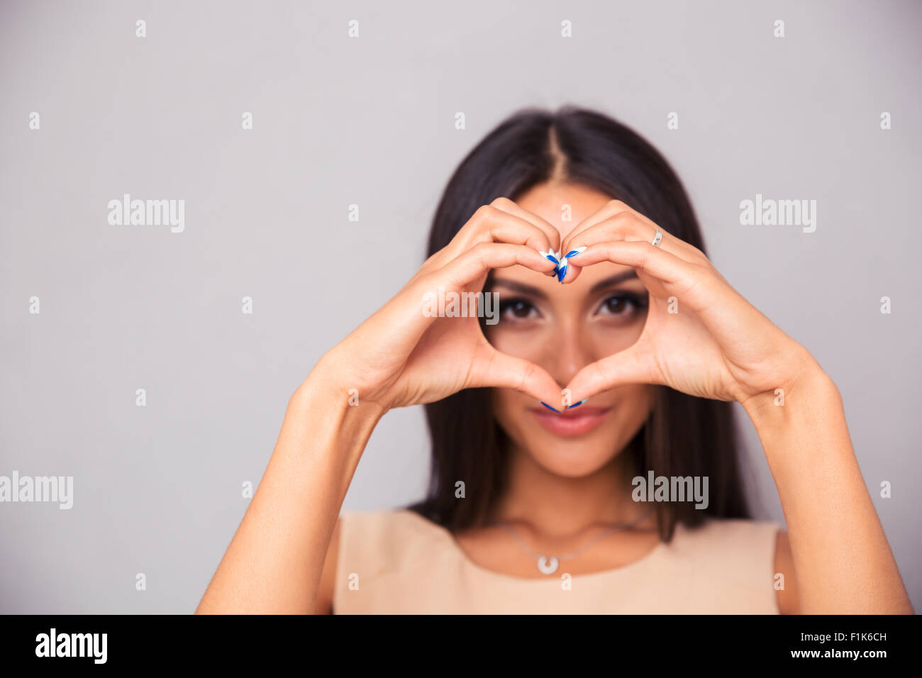 Portrait of a young charming woman making heart with fingers over gray ...