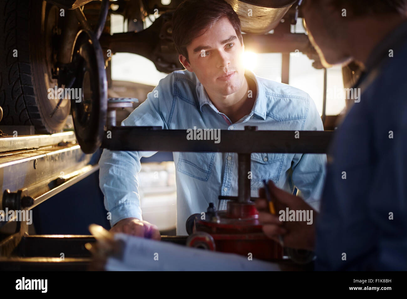 Mechanic and customer talking under car in auto repair shop Stock Photo ...