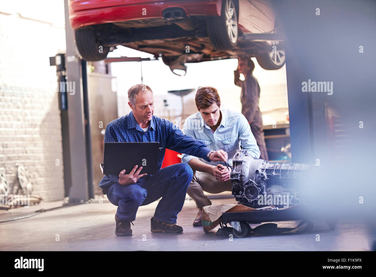 Mechanic and customer with laptop examining engine in auto repair shop ...