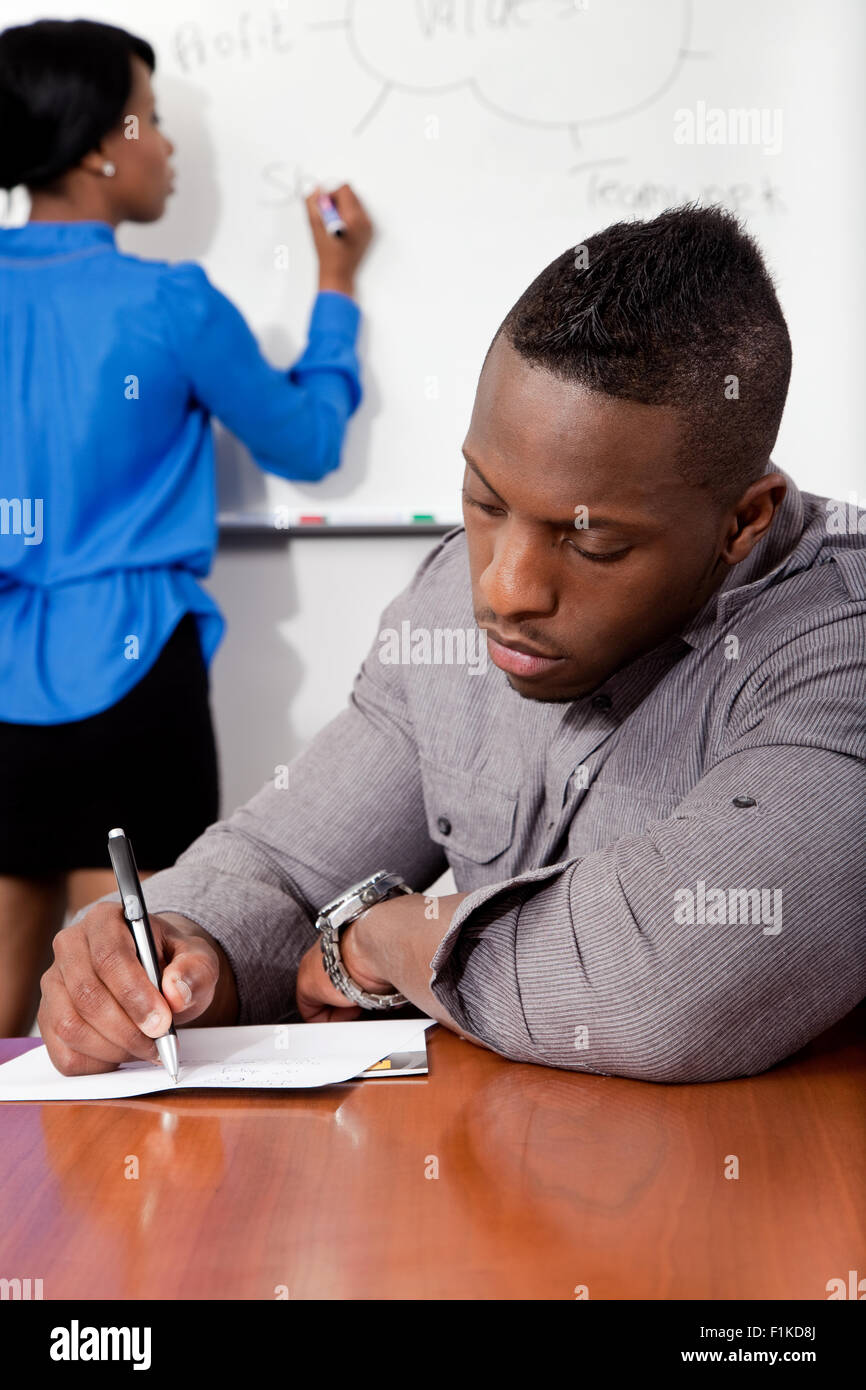 Black businessman taking notes while his female colleague gives a ...