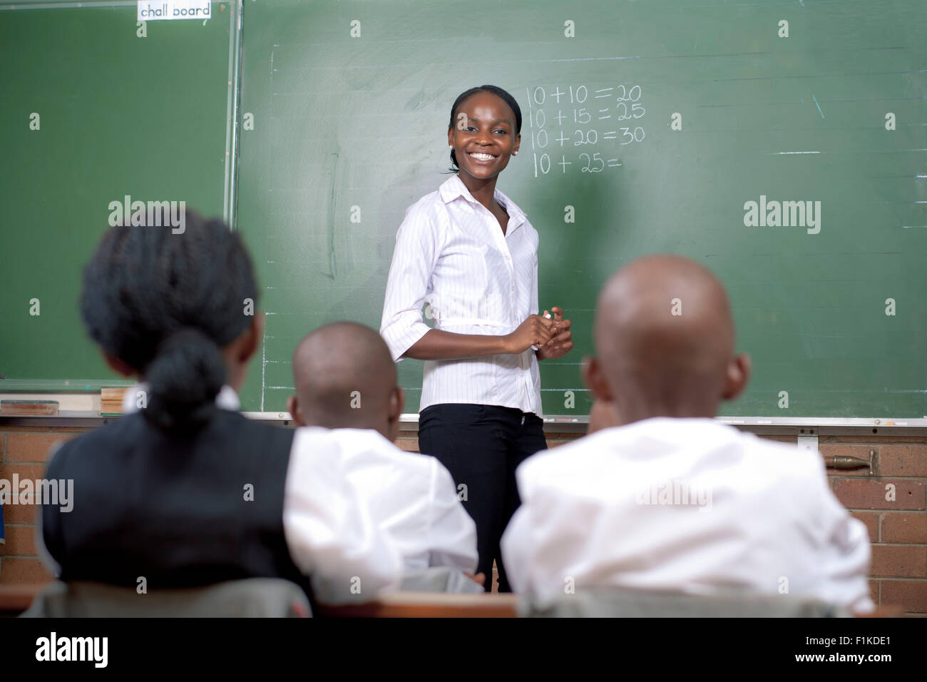 African teacher writing on a chalkboard, teaching her class Stock Photo ...