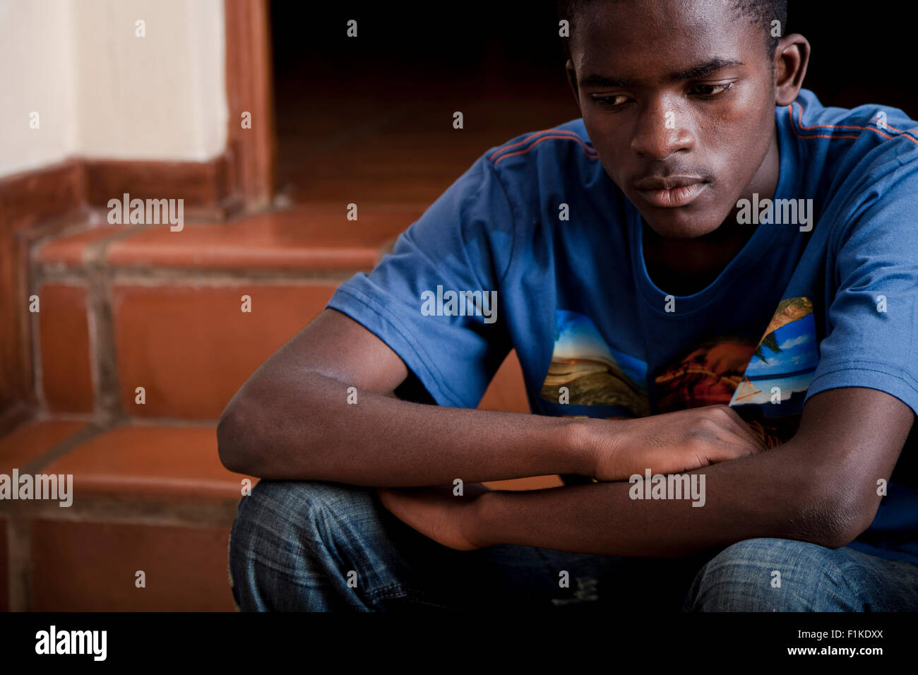 An African teenage boy sitting outside, looking somber Stock Photo - Alamy