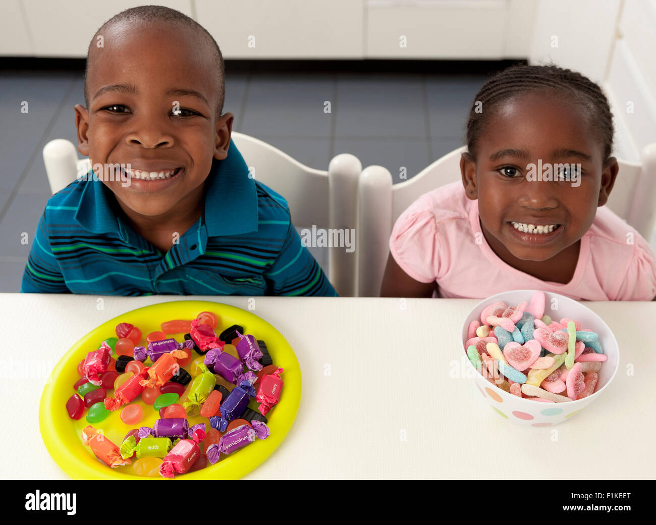 Two African children sit together in the kitchen eating sweets and ...