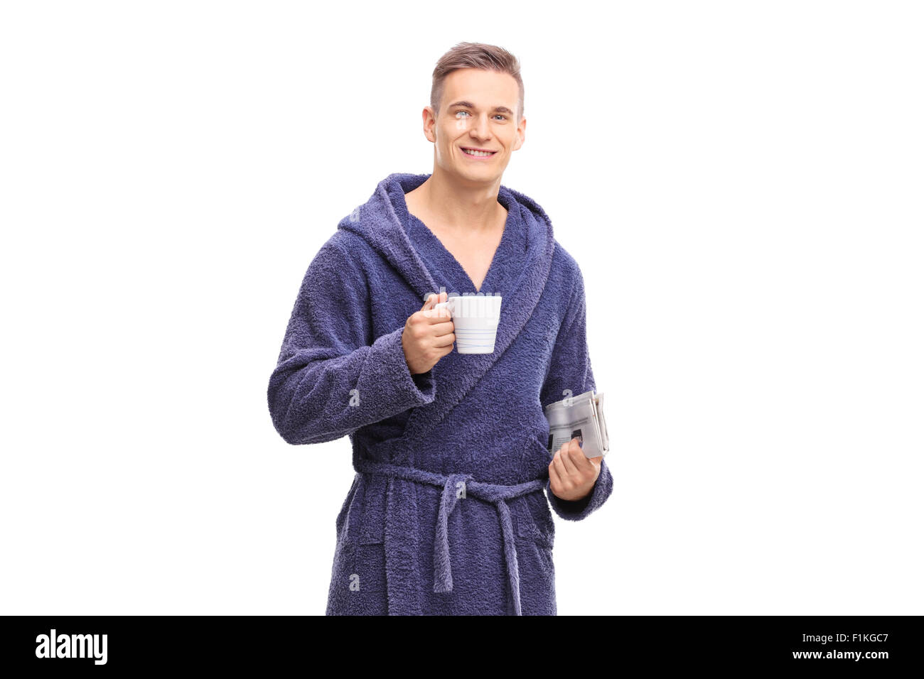 Relaxed young man in a bathrobe holding a cup of coffee and a newspaper ...