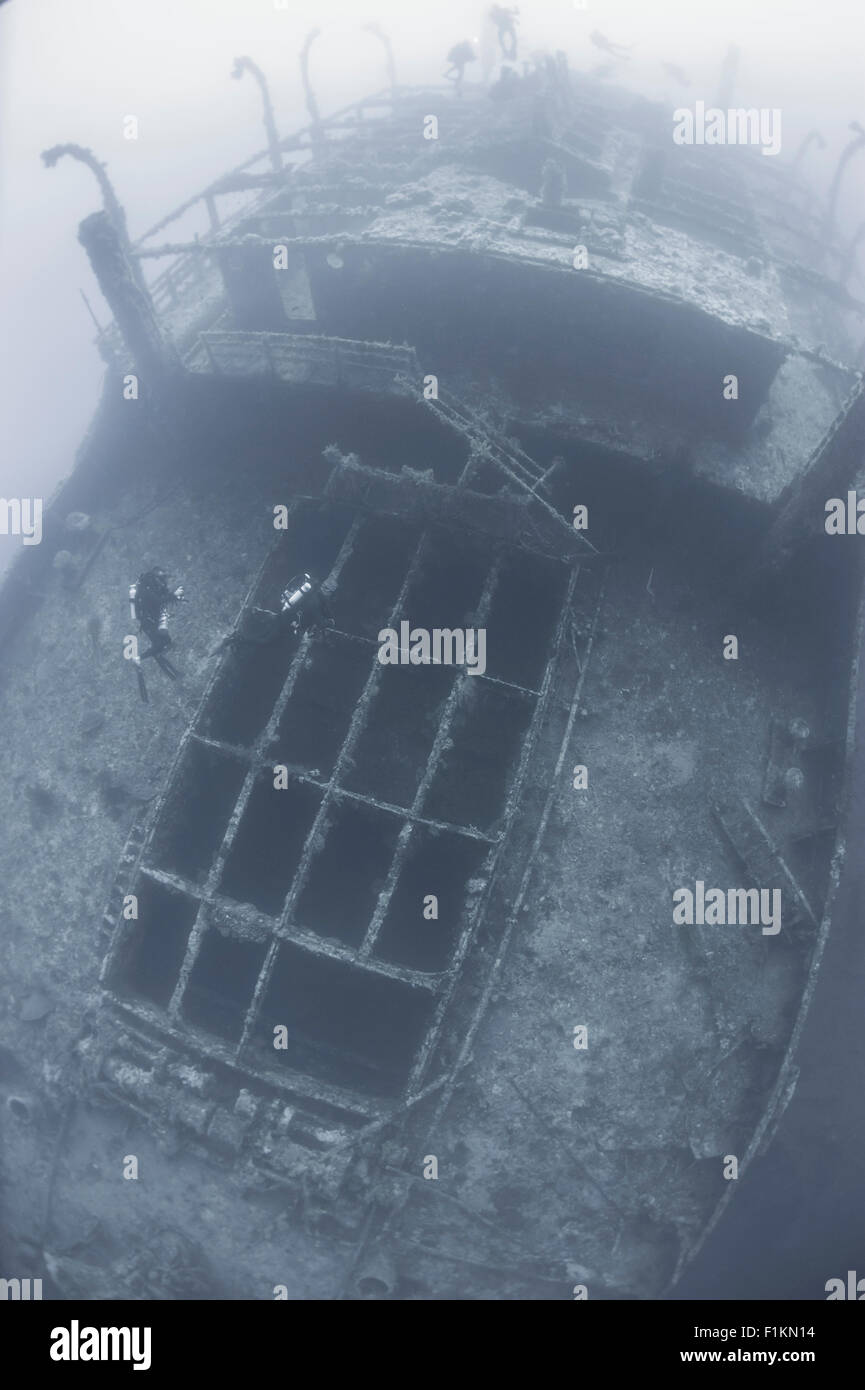 Technical scuba divers exploring a large deep underwater shipwreck ...