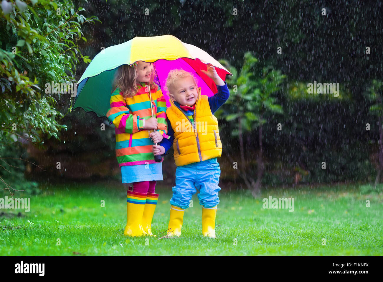 Little girl and boy with colorful umbrella playing in the rain. Kids ...