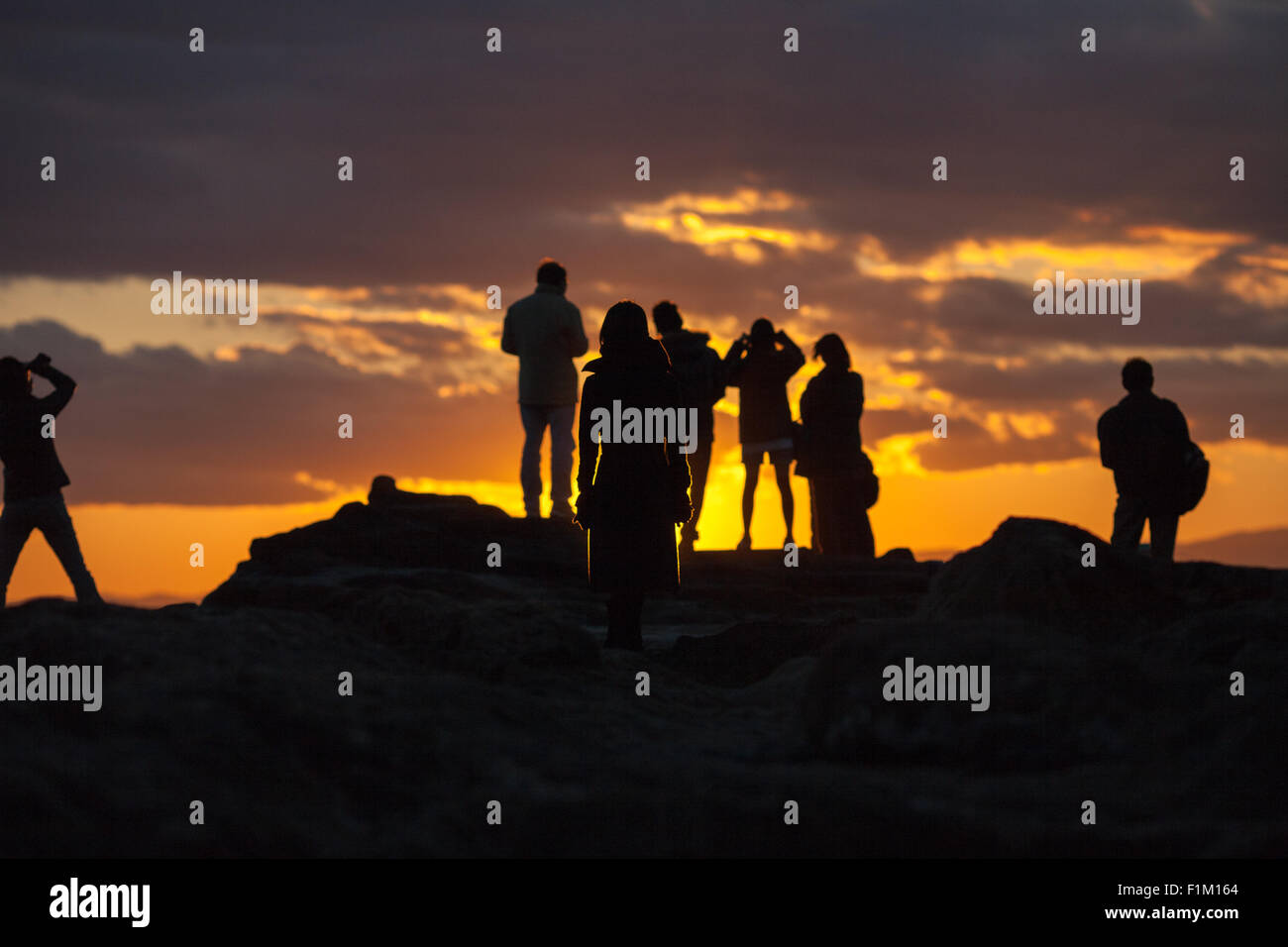 Silhouette of people watching sunset on rocks gold light Stock Photo ...
