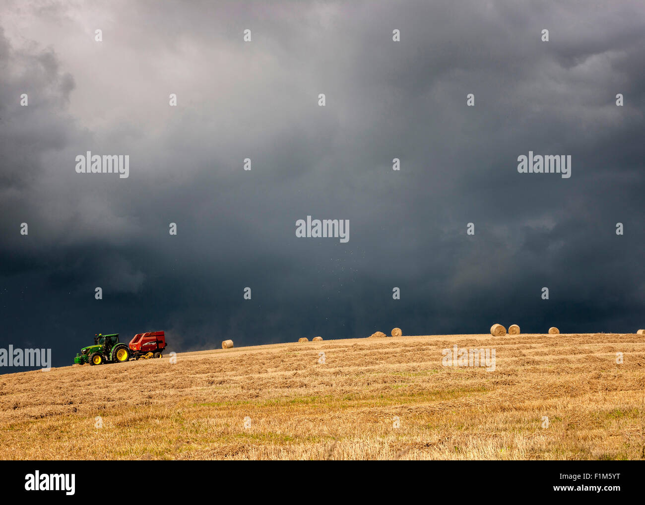 A tractor collecting hay bales under dark black stormy sky Stock Photo ...