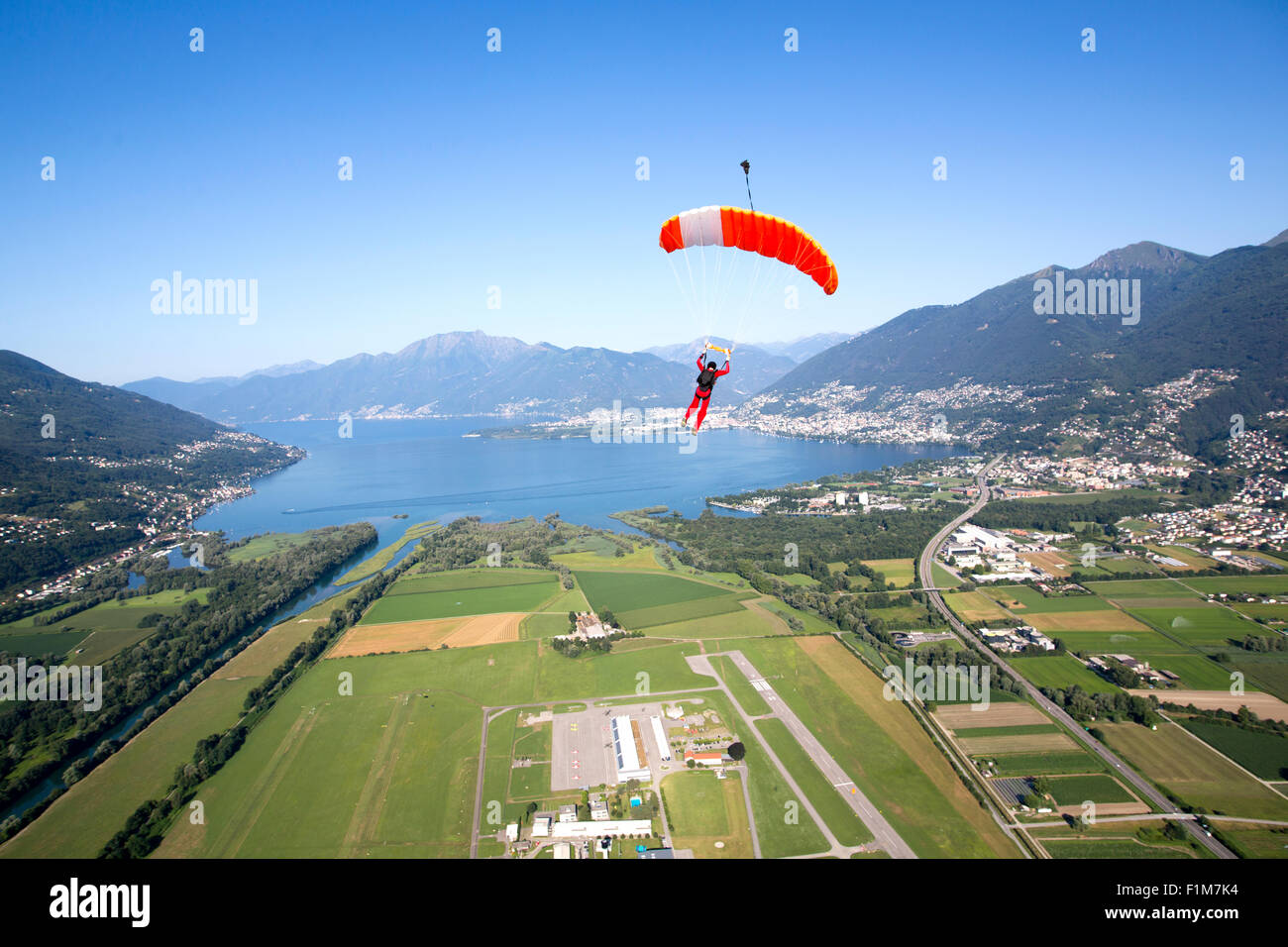 Skydiver is flying under canopy over an airport with a lake behind. She ...