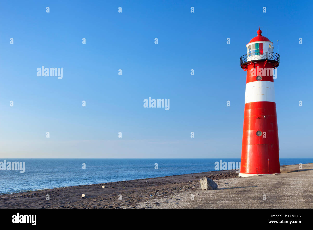 A red and white lighthouse at sea under a clear blue sky. Photographed ...