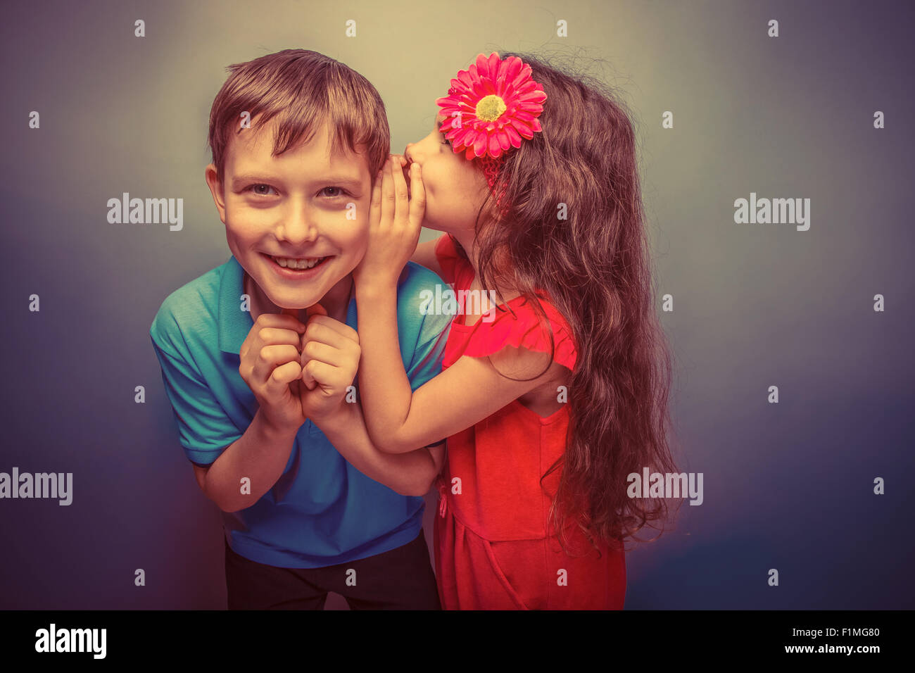 Teenage girl whispering in the ear of teen boys on a gray backg Stock ...