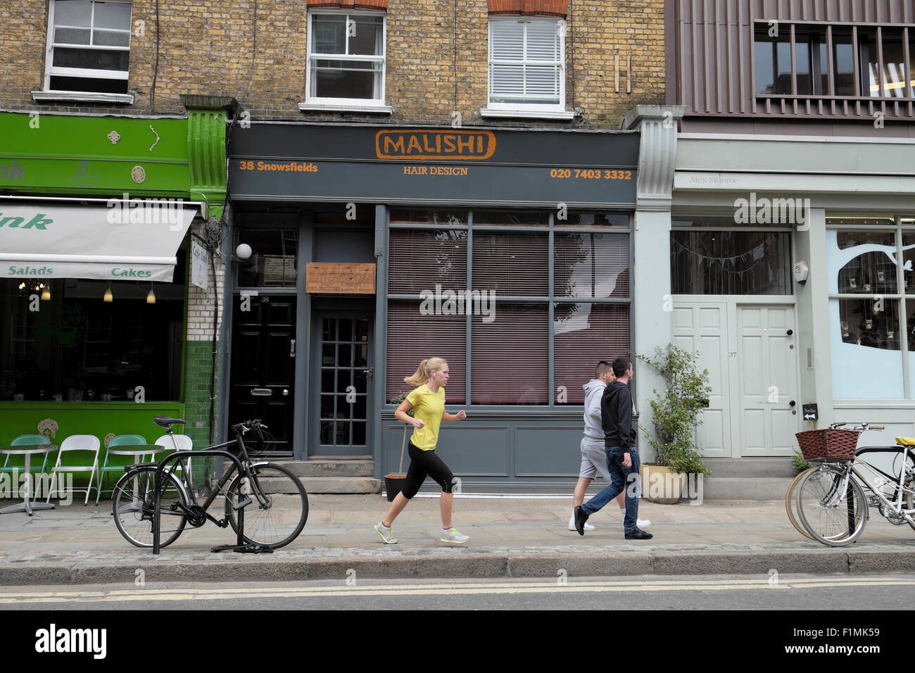 Woman jogger person wearing yellow jogging running past shops on street ...