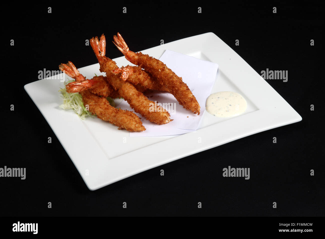 breaded prawns with vegetables and sauce in white plate on a black ...