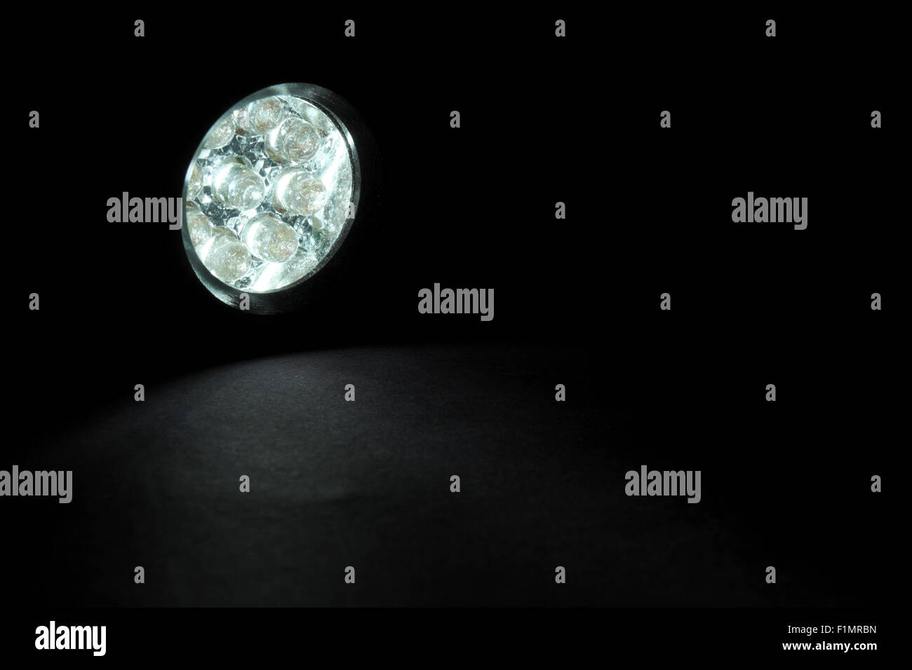 Turned-on LED flashlight casting a beam of light onto a dark background ...