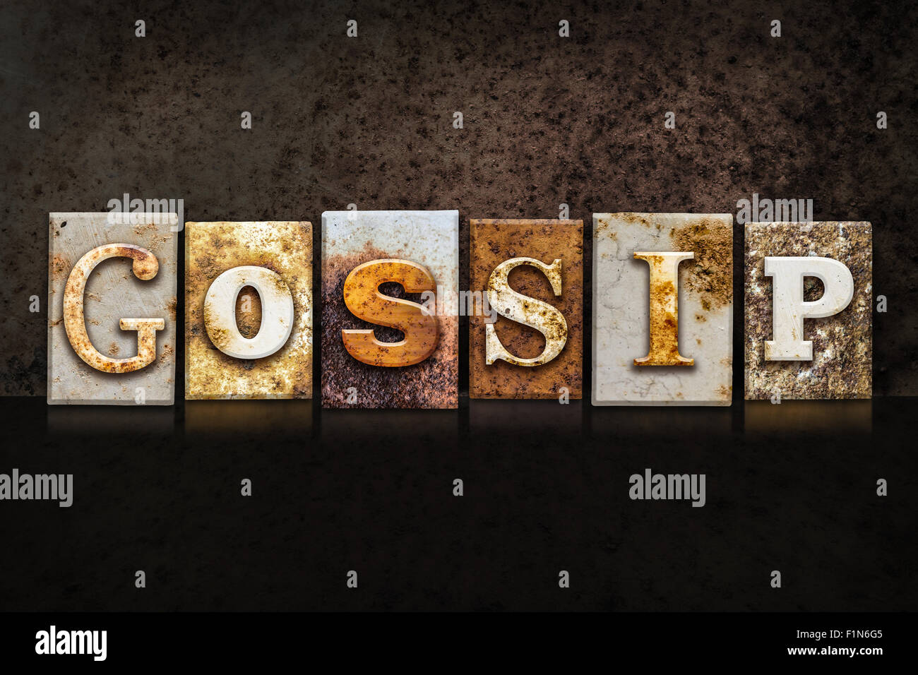The word "GOSSIP" written in rusty metal letterpress type on a dark ...