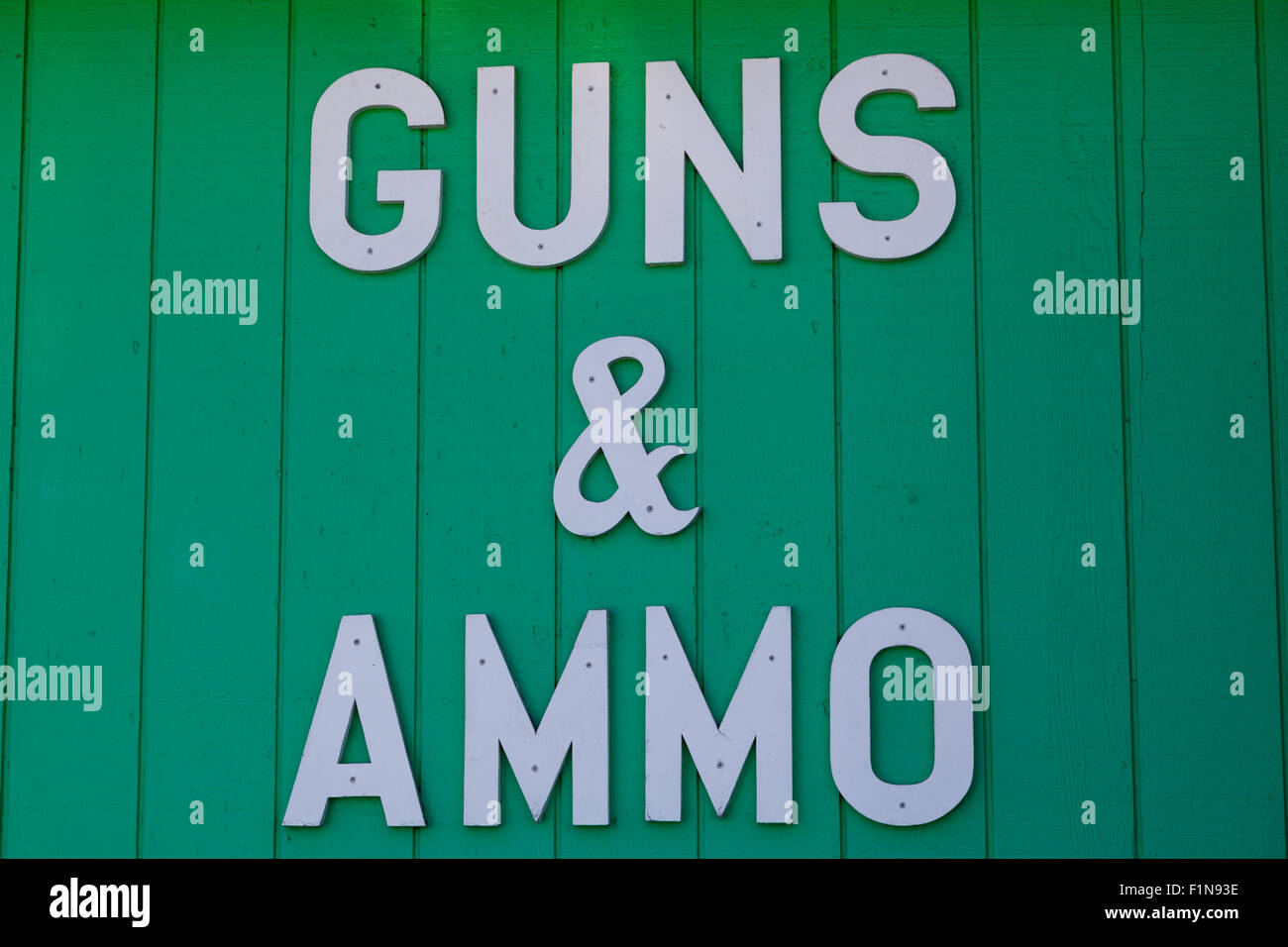 A white cutout letter sign nailed to a wall of a gun shop advertising ...