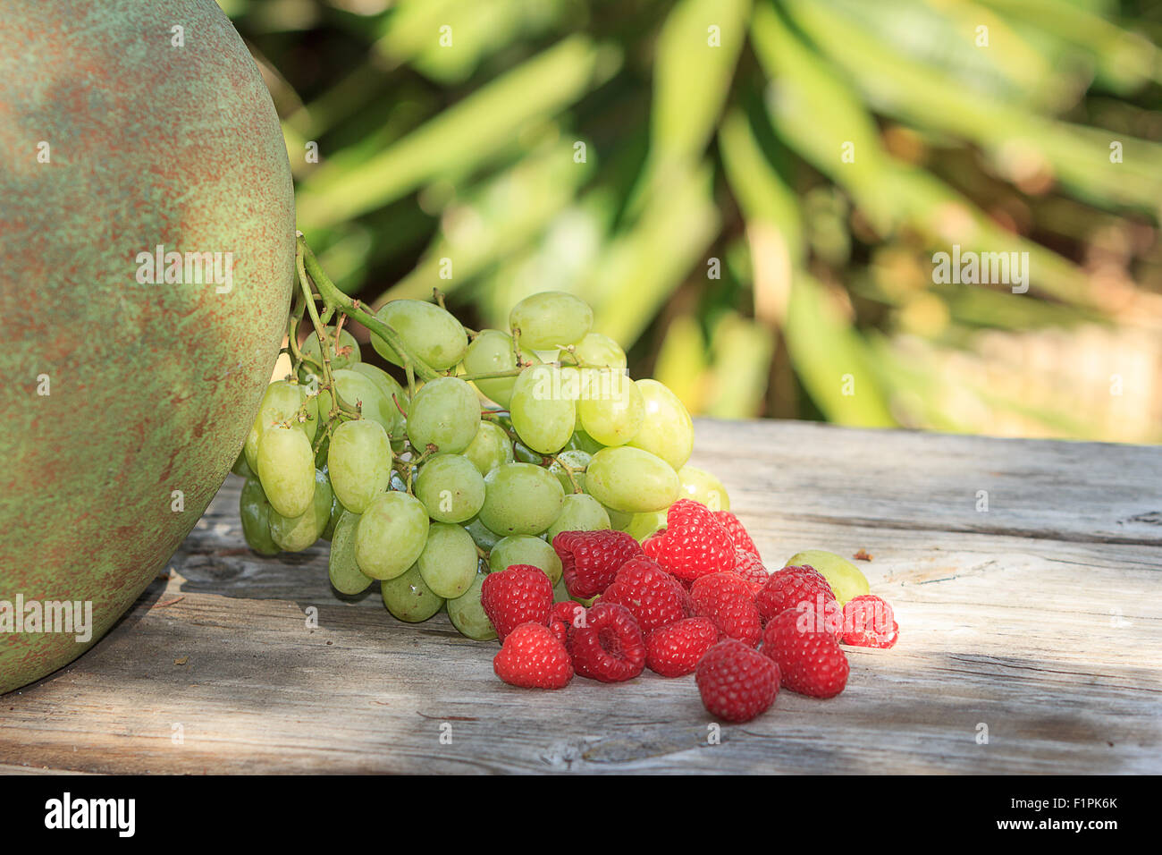 Green grapes and raspberries on a rustic wood table in summer Stock ...