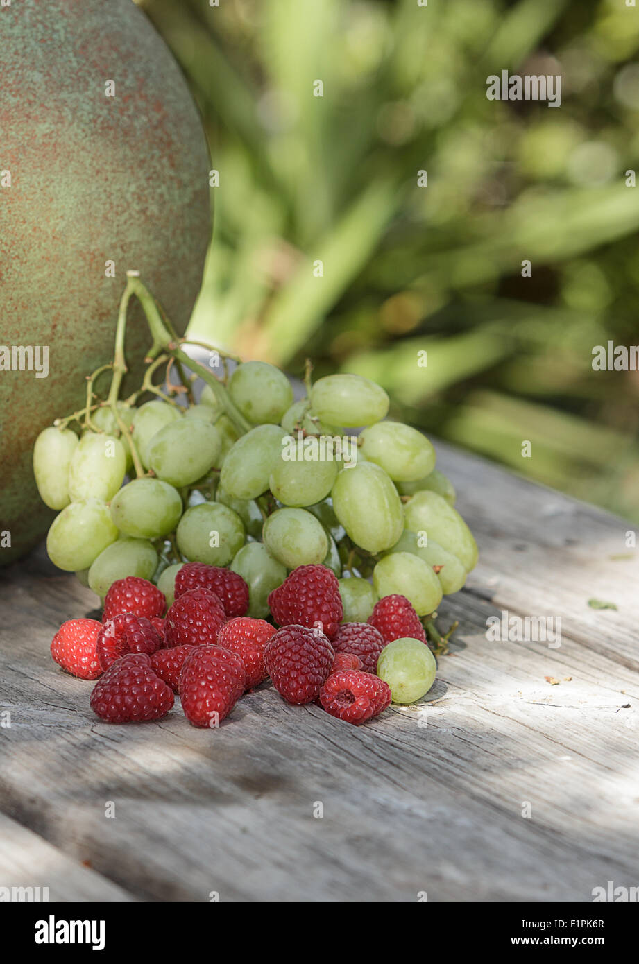 Green grapes and raspberries on a rustic wood table in summer Stock ...
