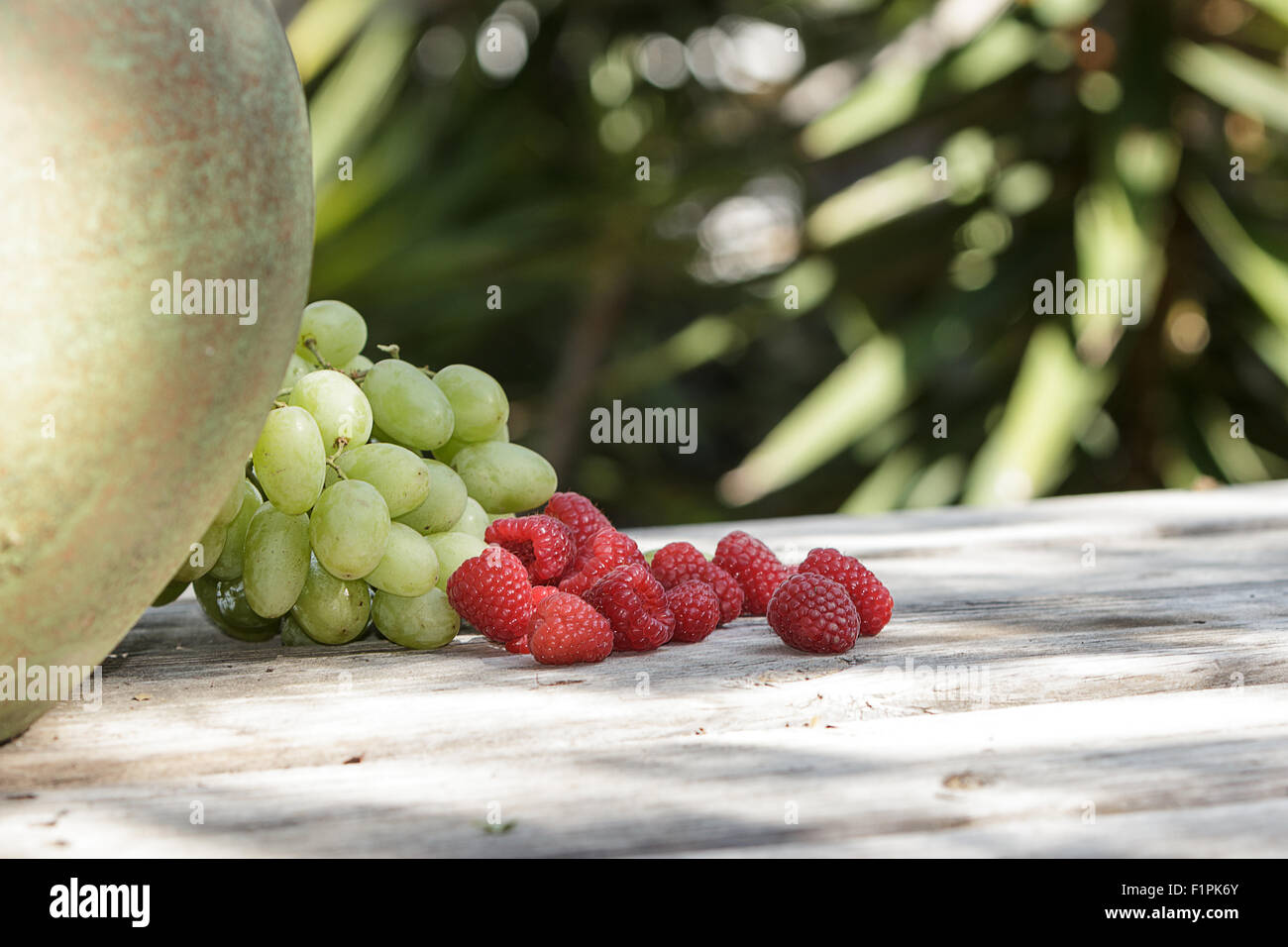 Green grapes and raspberries on a rustic wood table in summer Stock ...