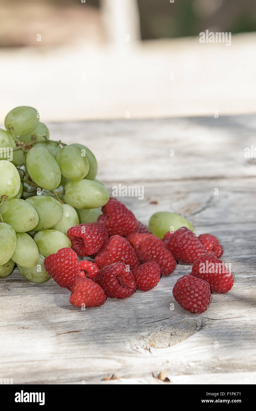 Green grapes and raspberries on a rustic wood table in summer Stock ...