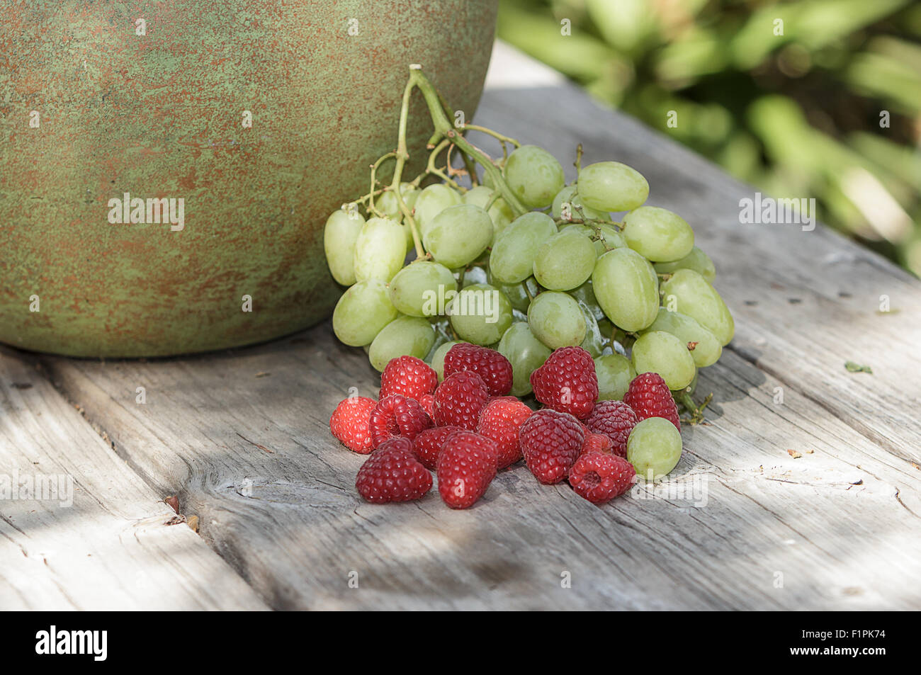 Green grapes and raspberries on a rustic wood table in summer Stock ...