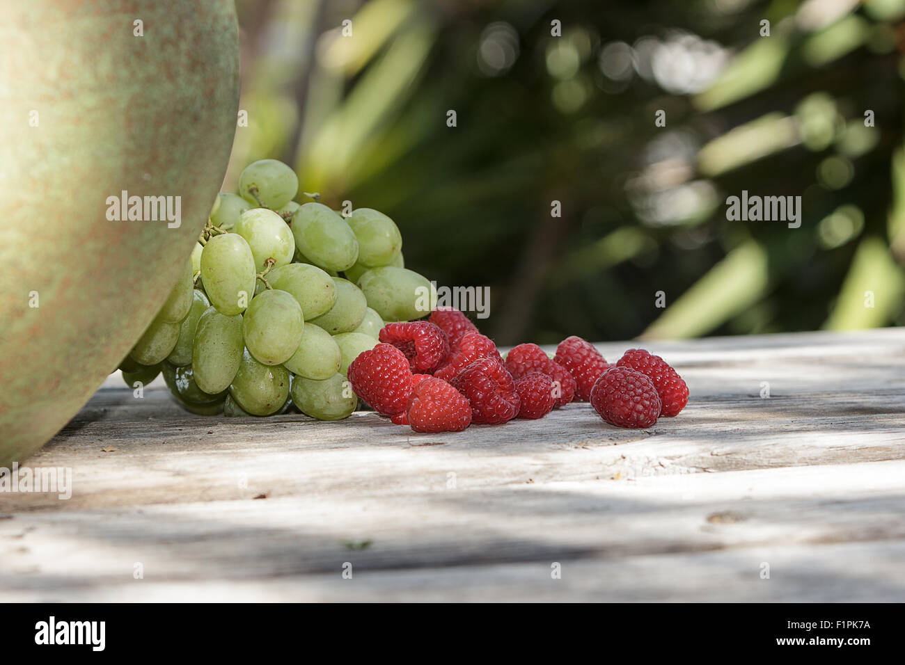 Green grapes and raspberries on a rustic wood table in summer Stock ...