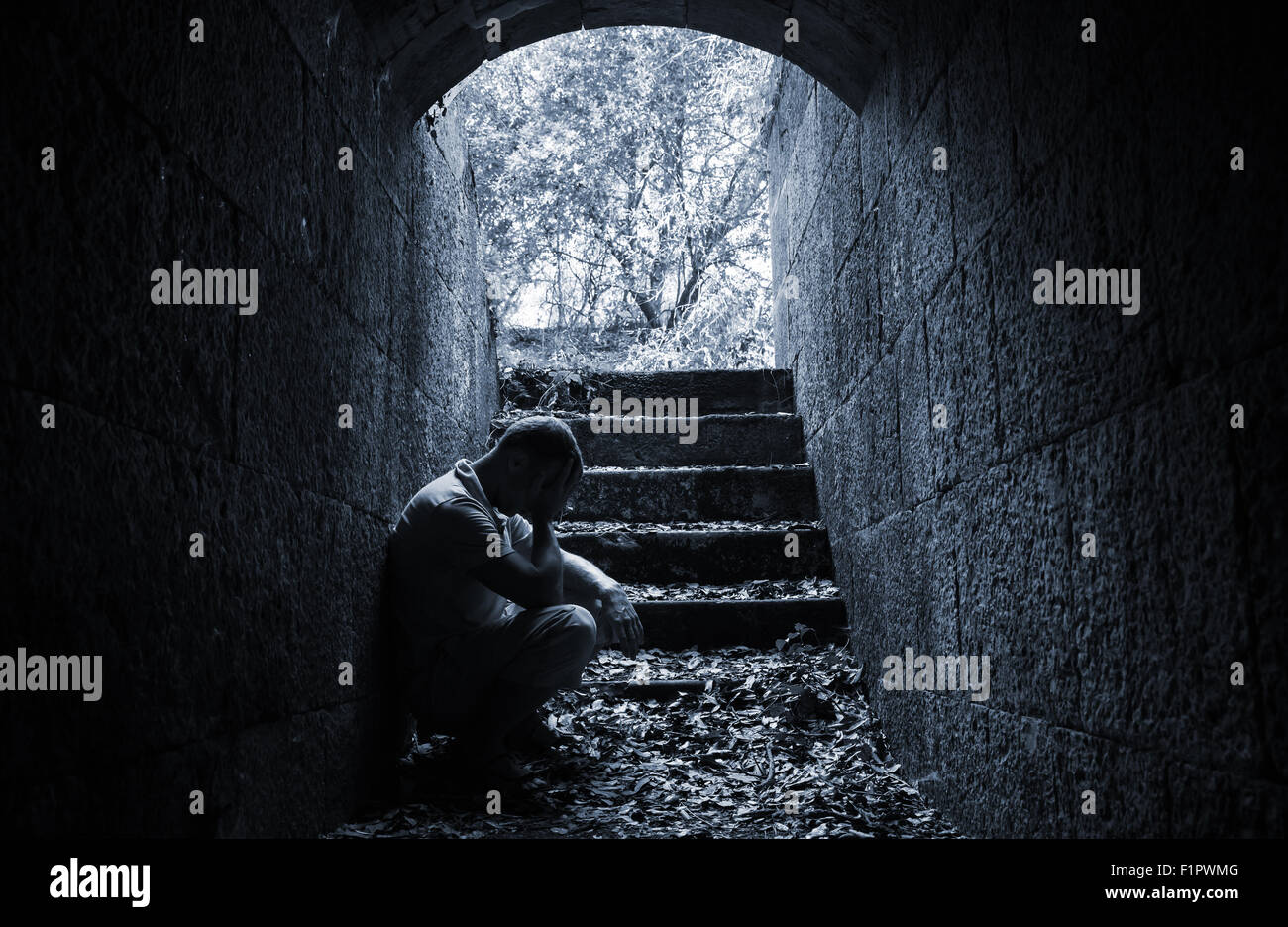 Young sad man sitting inside of dark stone tunnel, blue tonal ...