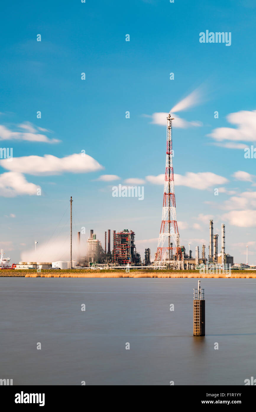 Long exposure shot of a refinery with tall flare stack in the port of ...