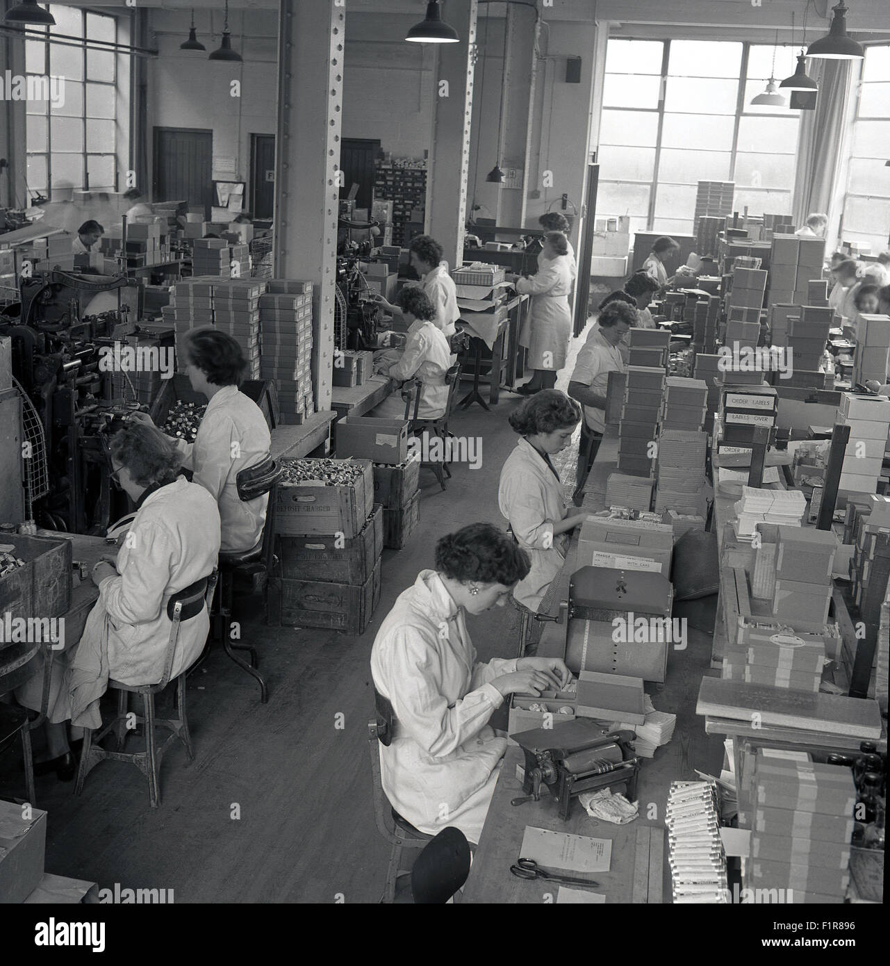 Historical, 1950s, female workers in white-coats sit at benches sorting ...