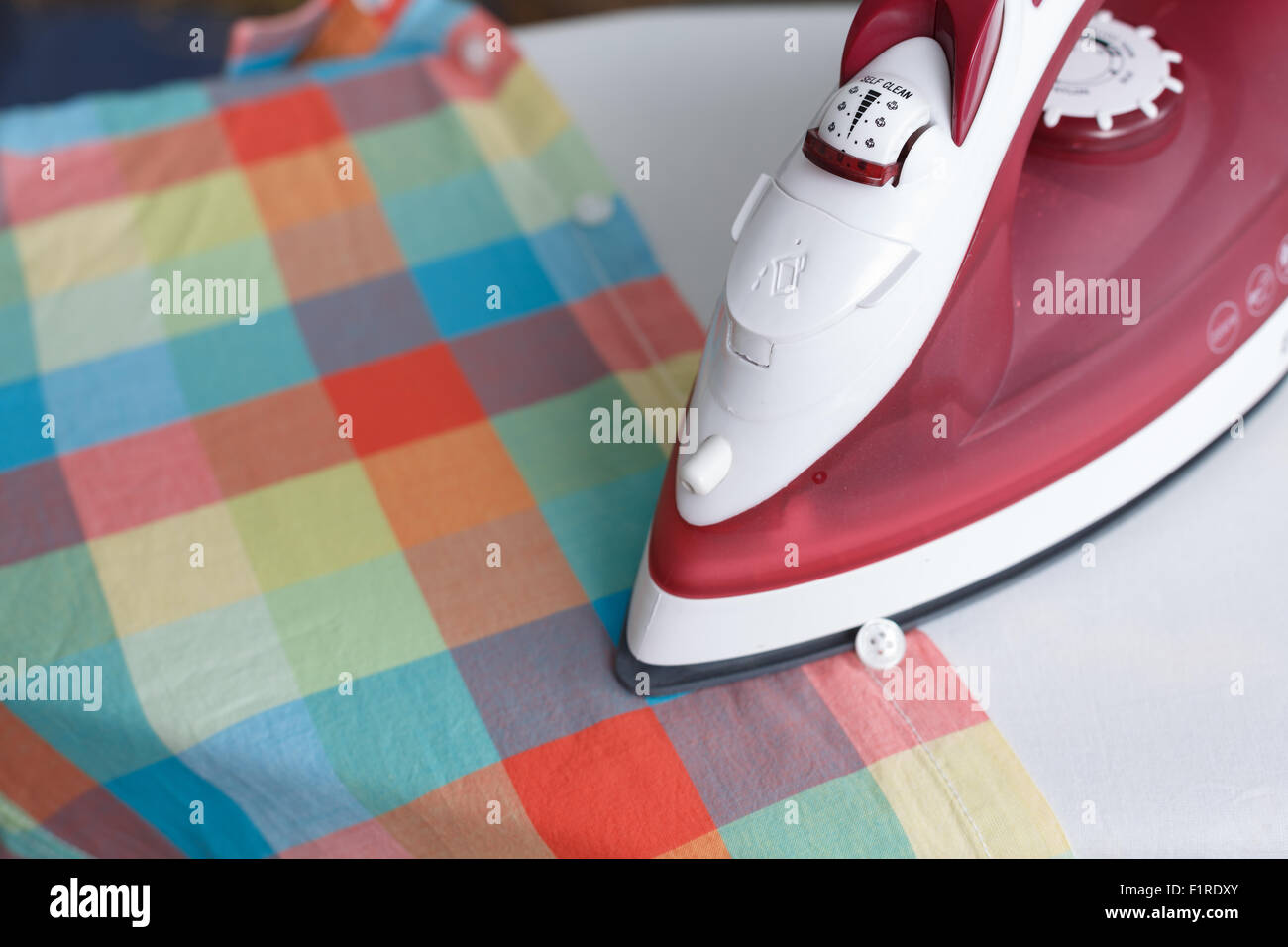 Close up of iron on ironing board near the plaid shirt. Focus on steam ...