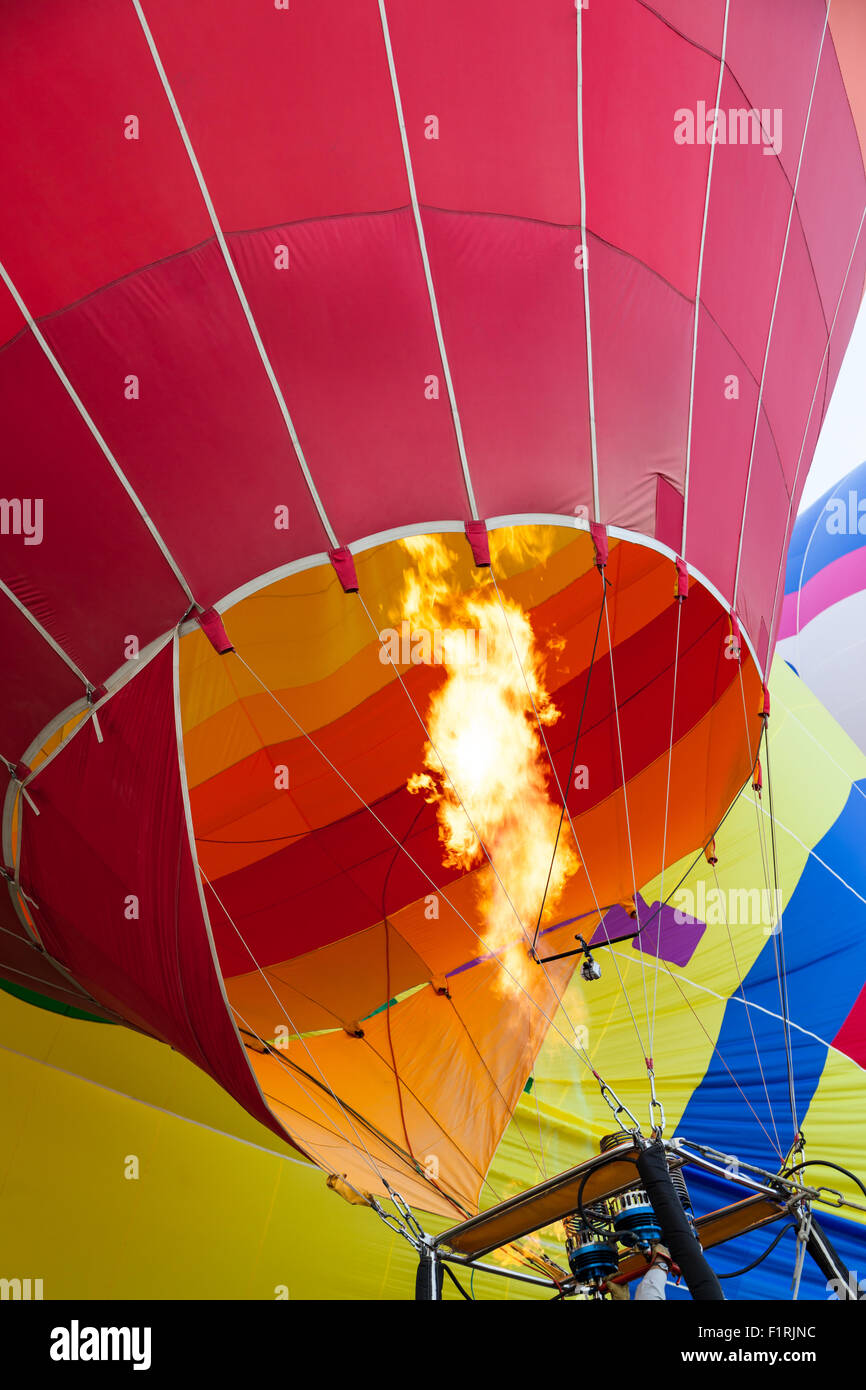 Close up of a hot air balloon flame inflating a red balloon with other ...