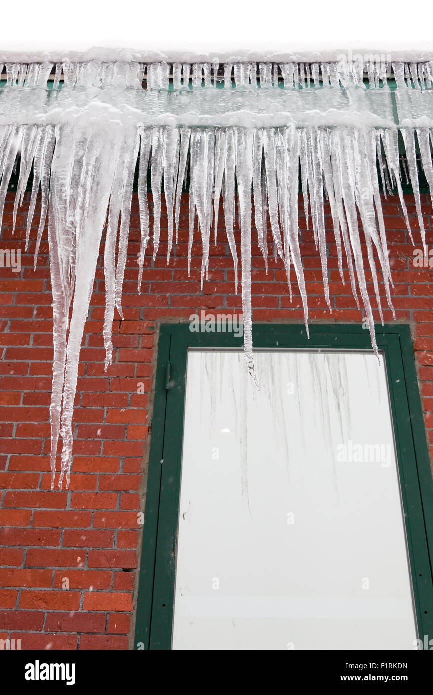 Long delicate fingers of ice hang from a gutter atop a red brick ...