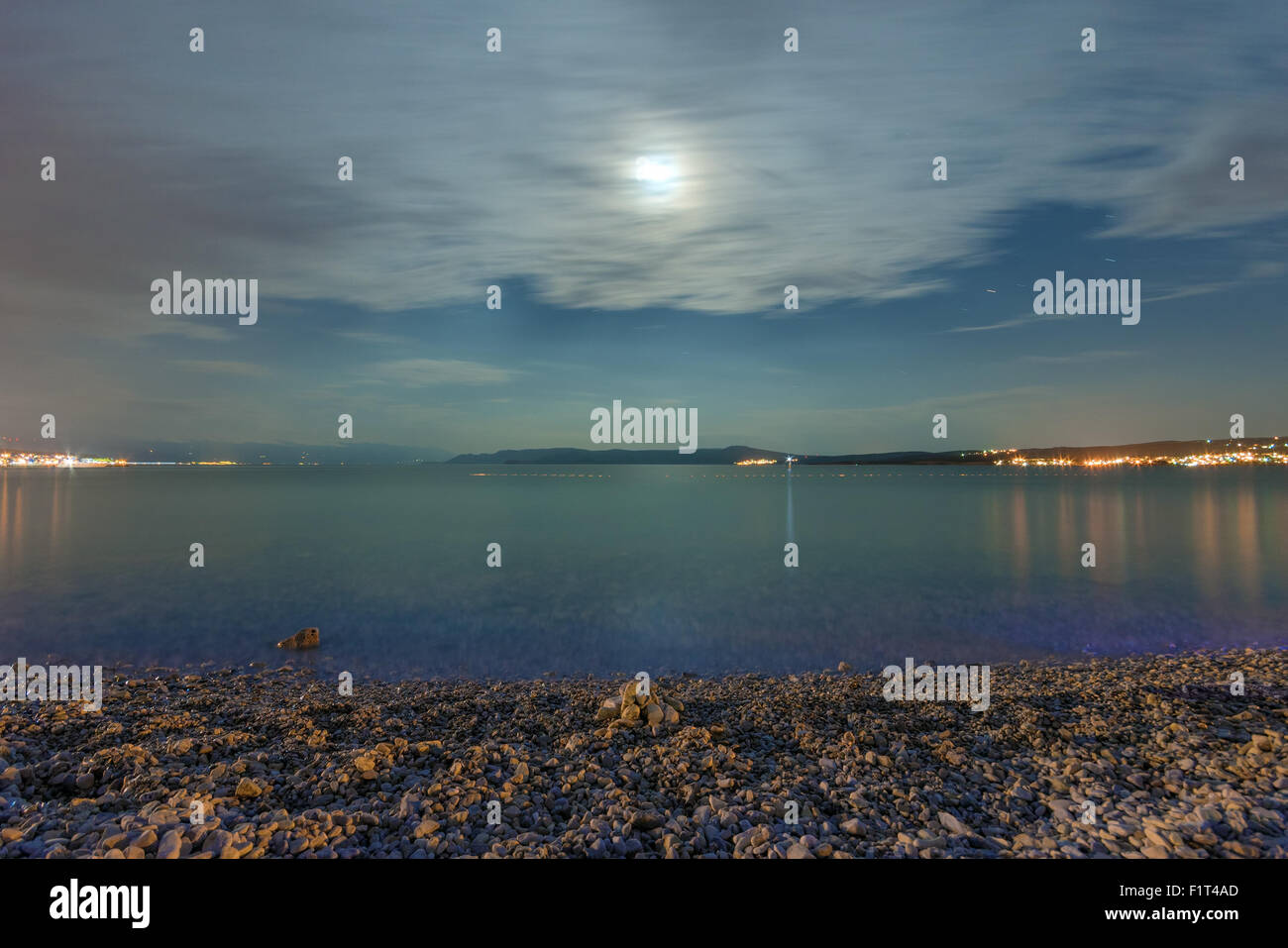 Empty pebble beach at night illuminated by the moonlight with islands ...