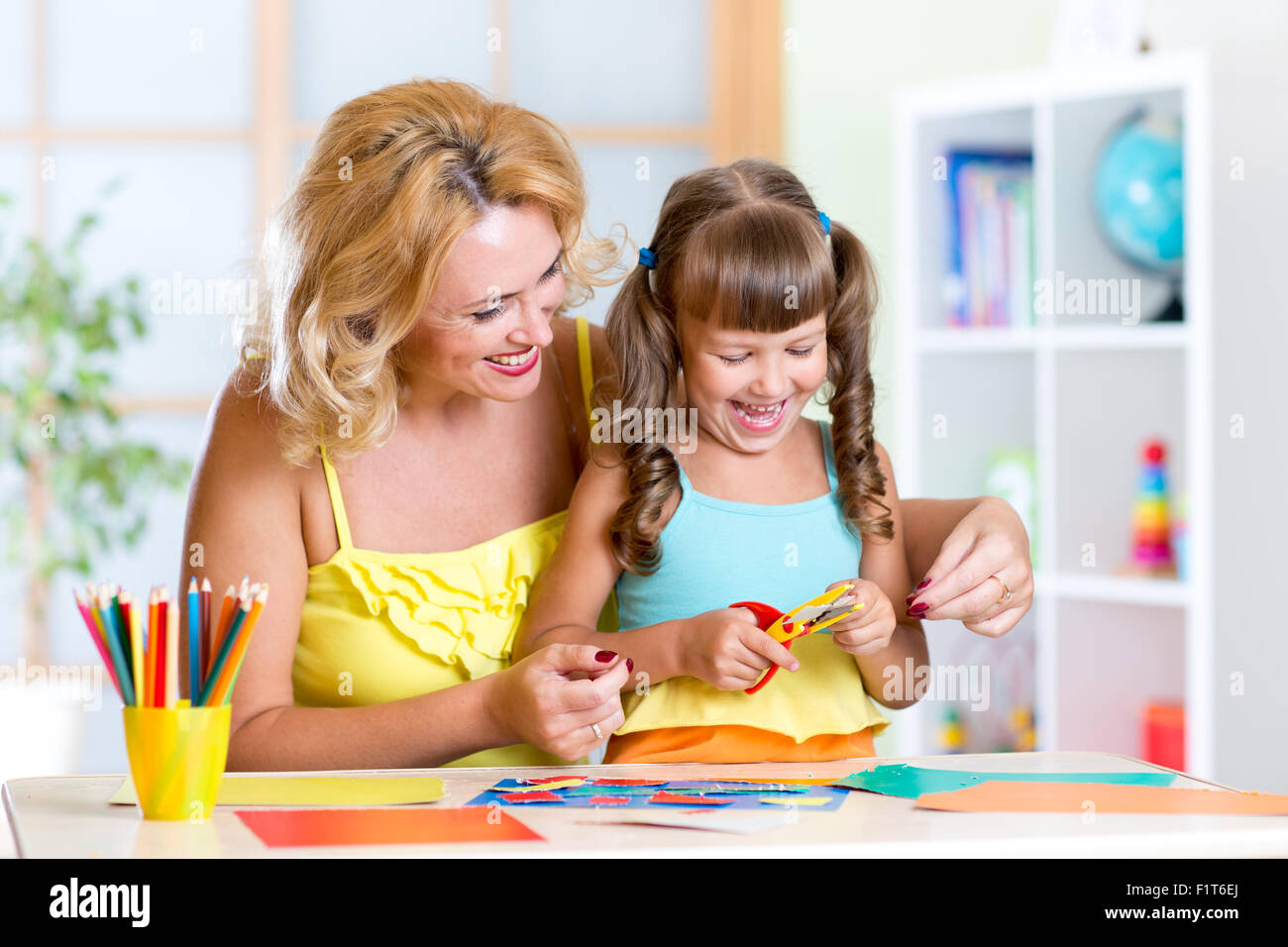 Child with woman cutting out scissors paper in preschool Stock Photo ...
