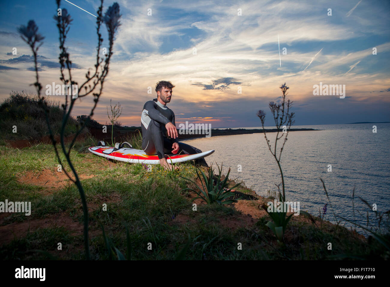 Young man sitting on surfboard Stock Photo - Alamy