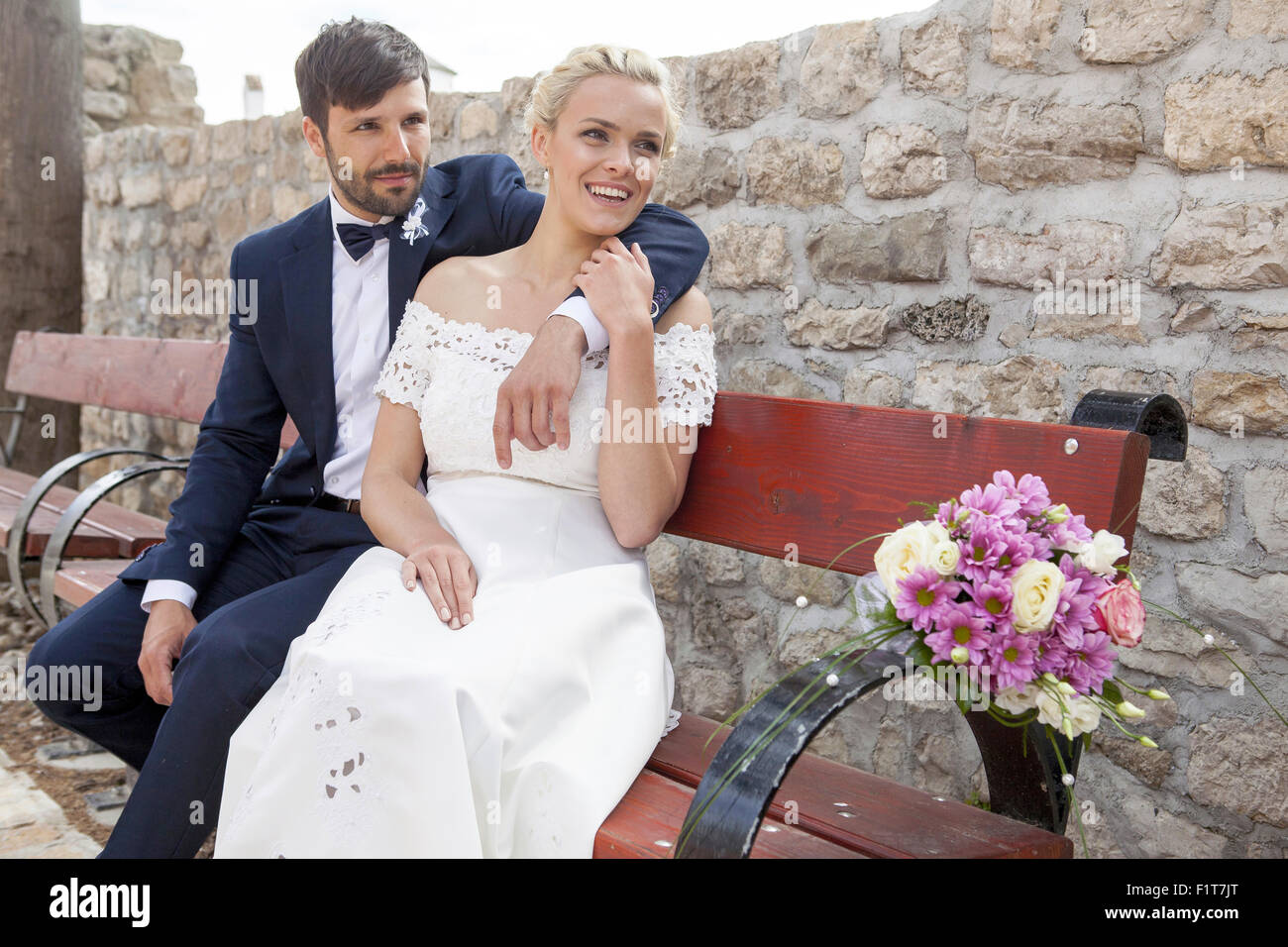 Bride and groom on bench smiling happily Stock Photo - Alamy