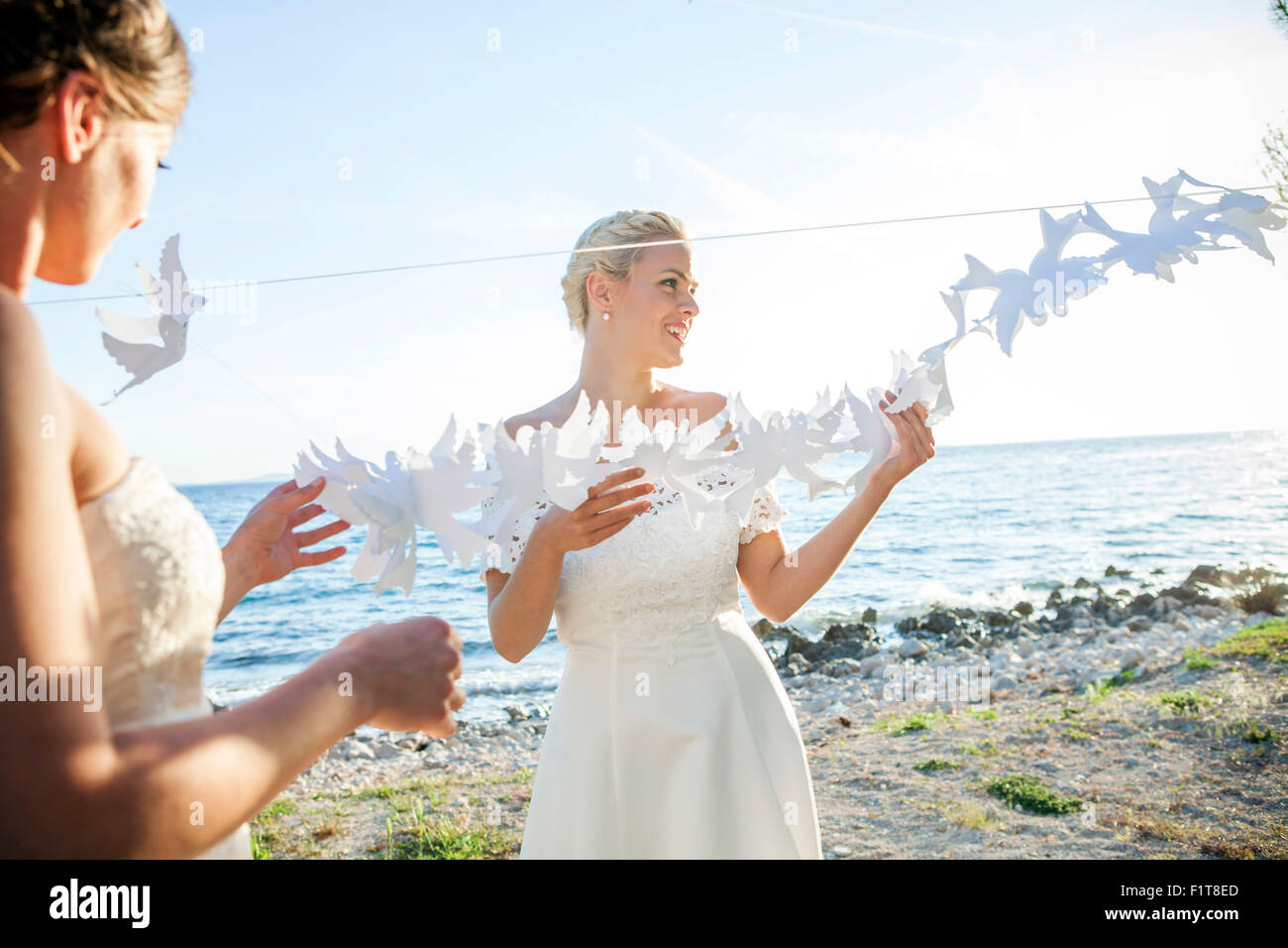 Bride and bridesmaid playing with white paper cut out outdoors Stock ...