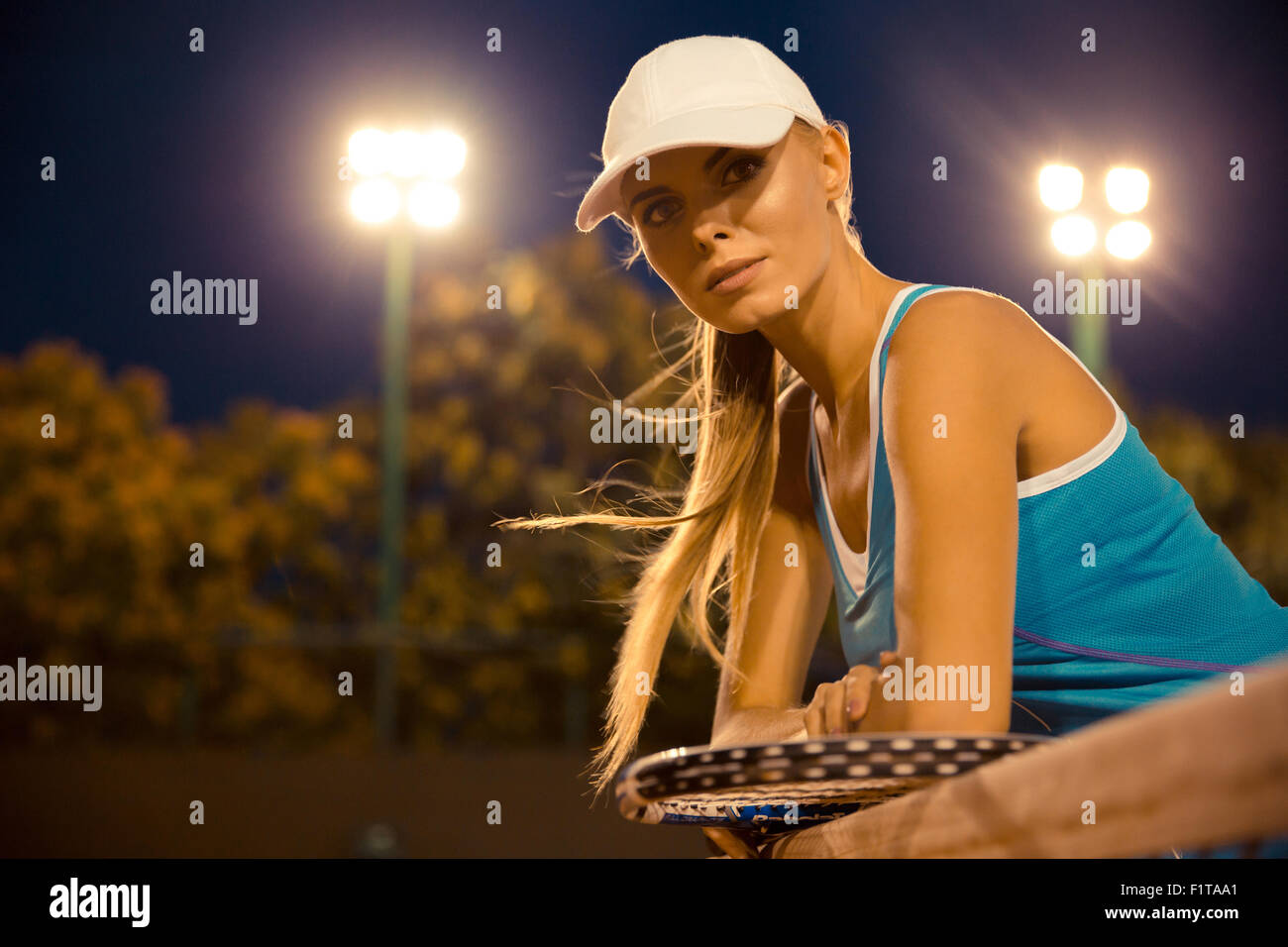Portrait of a beautiful female tennis player standing outdoors at night ...