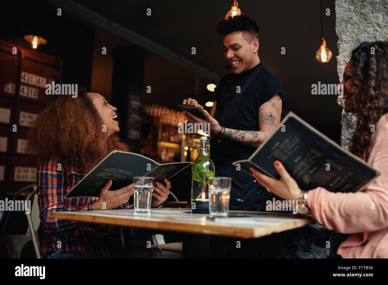 Cheerful two young women sitting at cafe holding menu card giving order ...