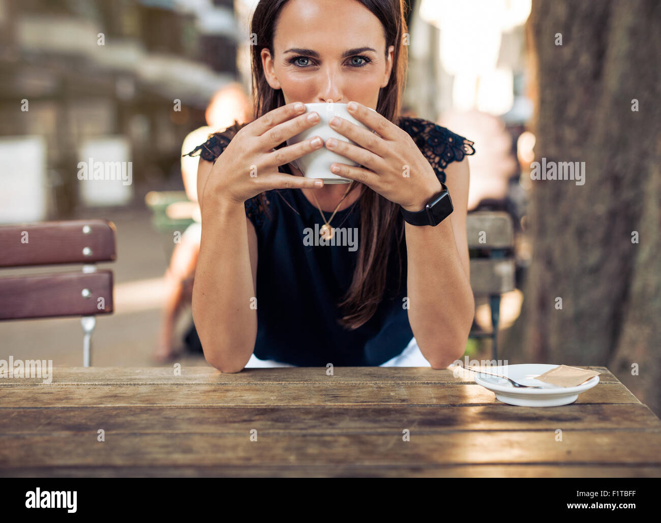 Young woman drinking coffee at a cafe and looking at the camera ...