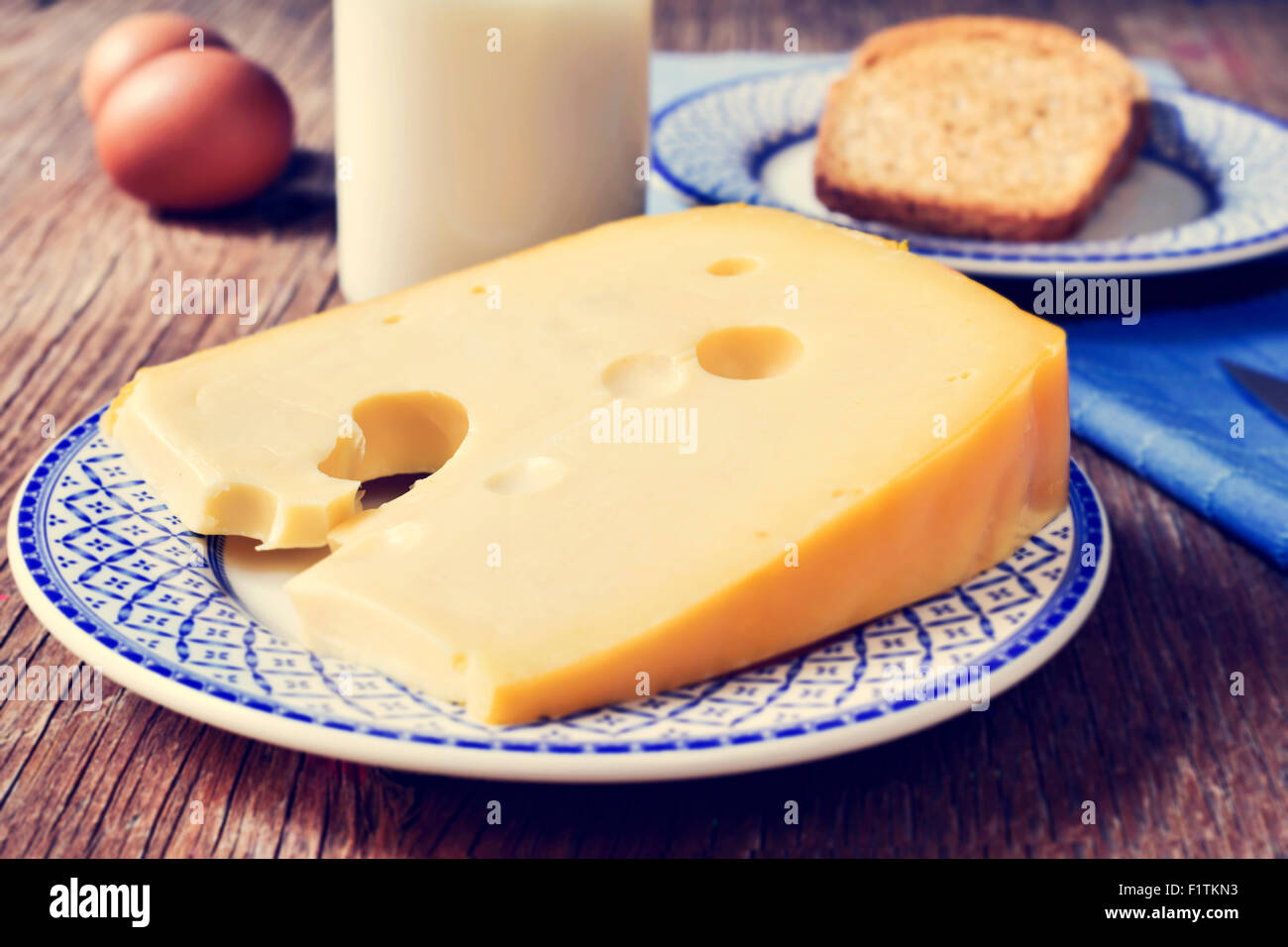 closeup of a piece of Swiss cheese in a plate, a bottle with milk, some ...