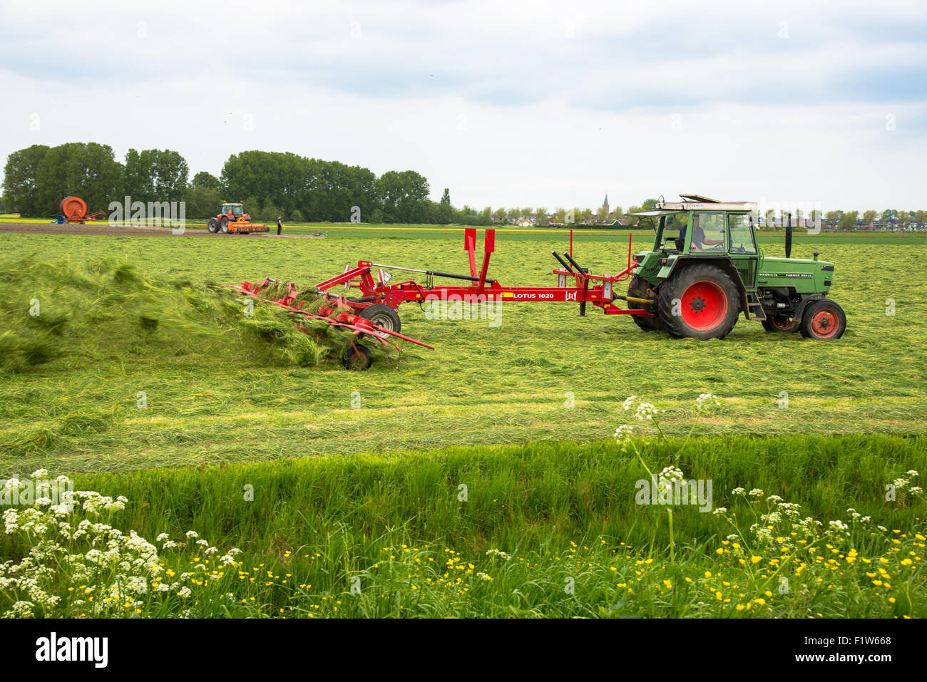 farmer with tractor at his farmland turning grass to dry in the sun ...