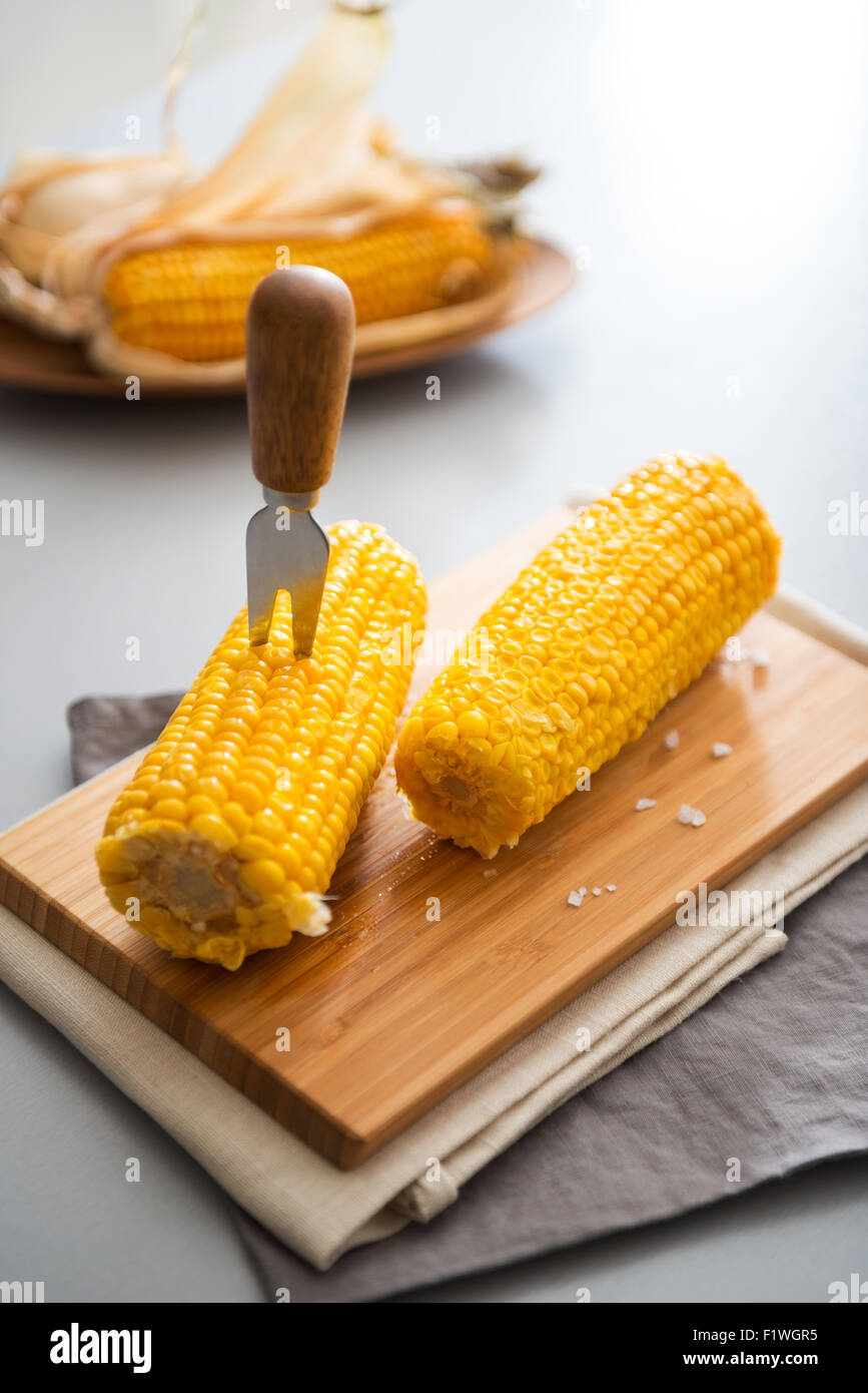 Ready, set, eat... Two rich, yellow corncobs are sitting on a wooden ...