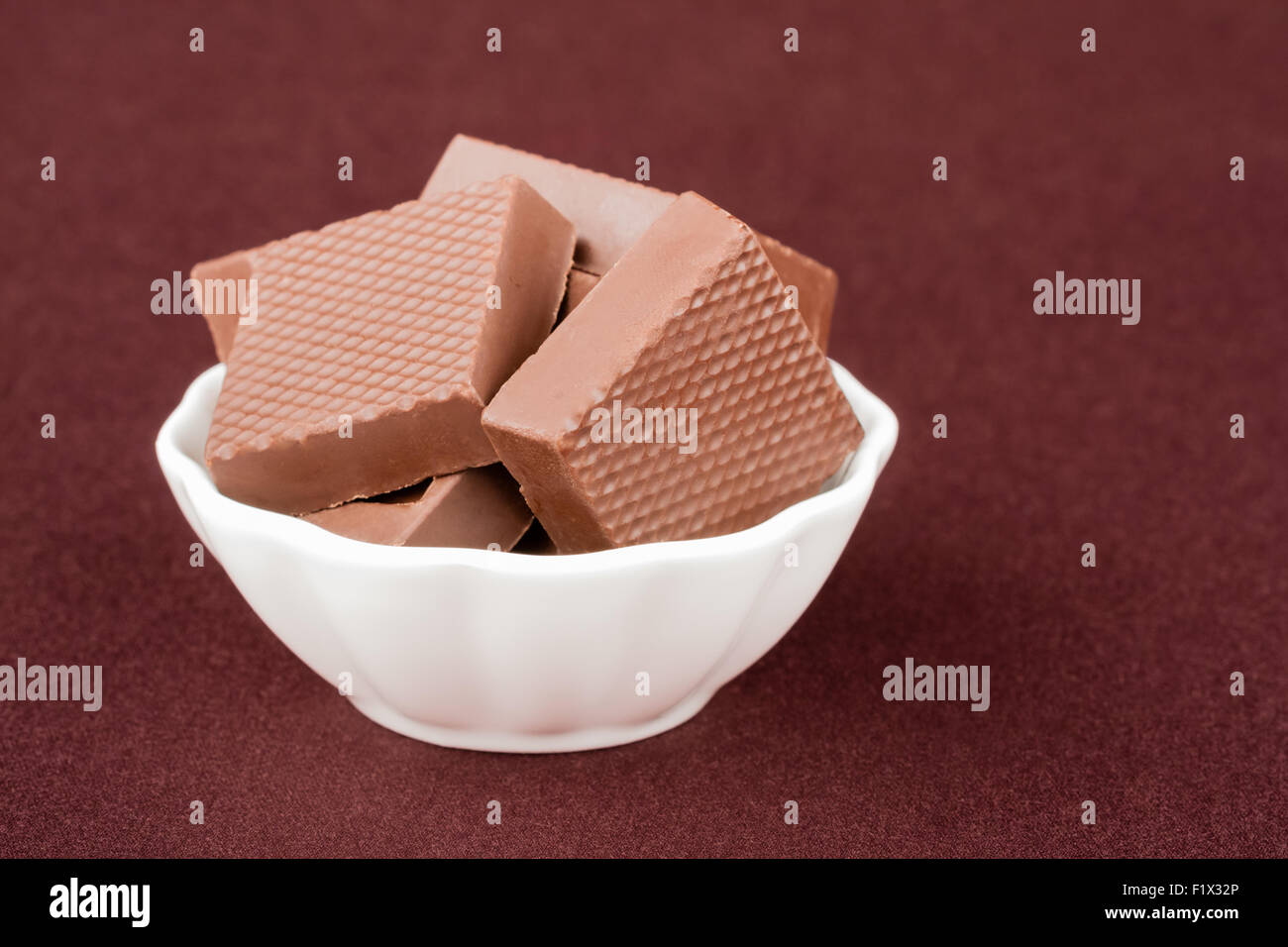 Chocolate squares in a white bowl on maroon background Stock Photo - Alamy