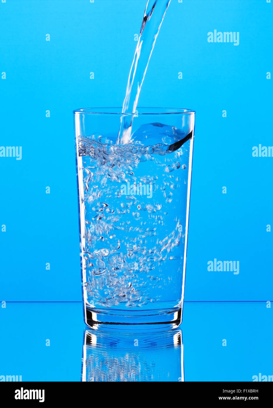Pouring water into glass on blue background Stock Photo - Alamy