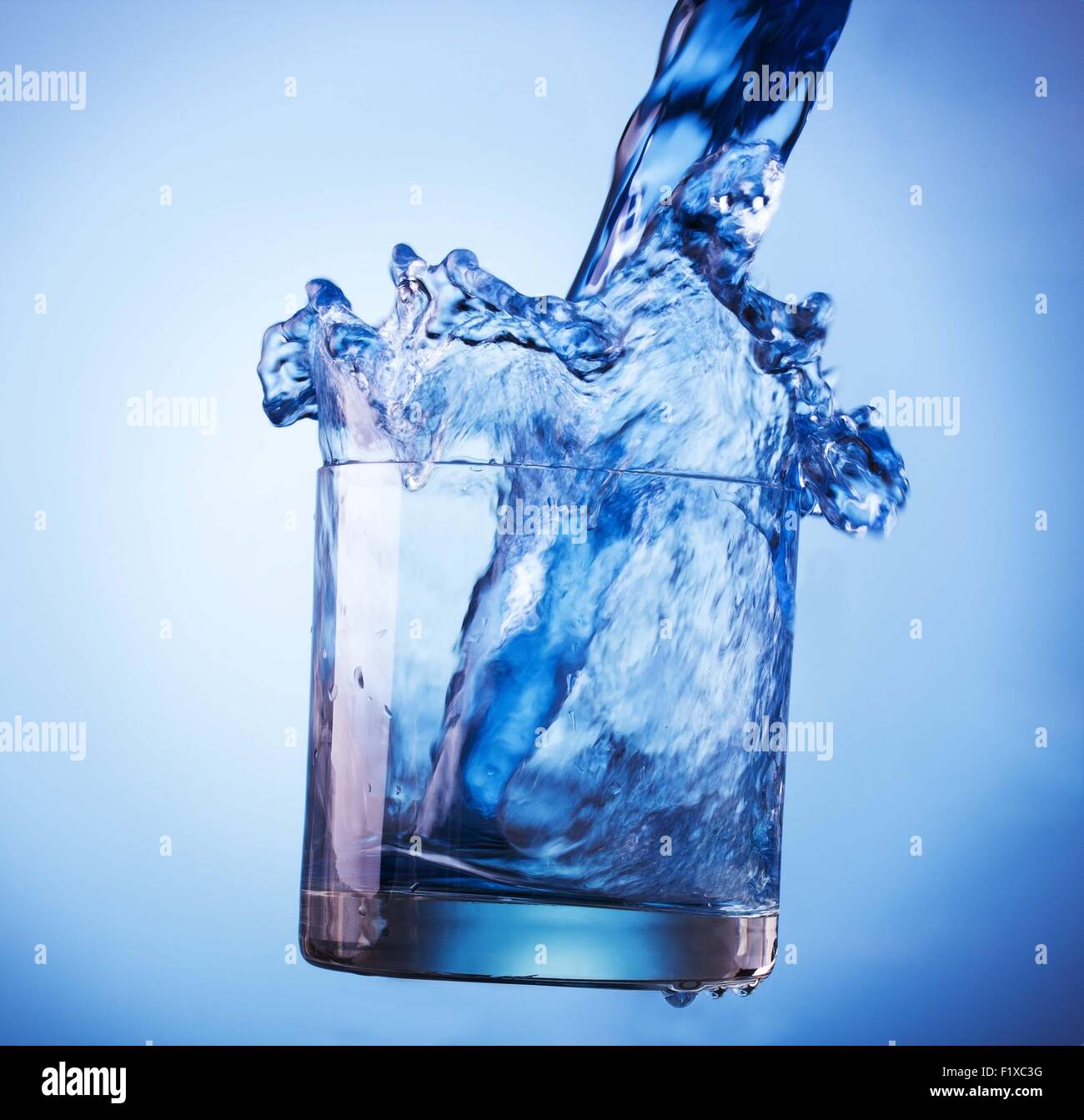 Pouring water into glass on blue background Stock Photo - Alamy