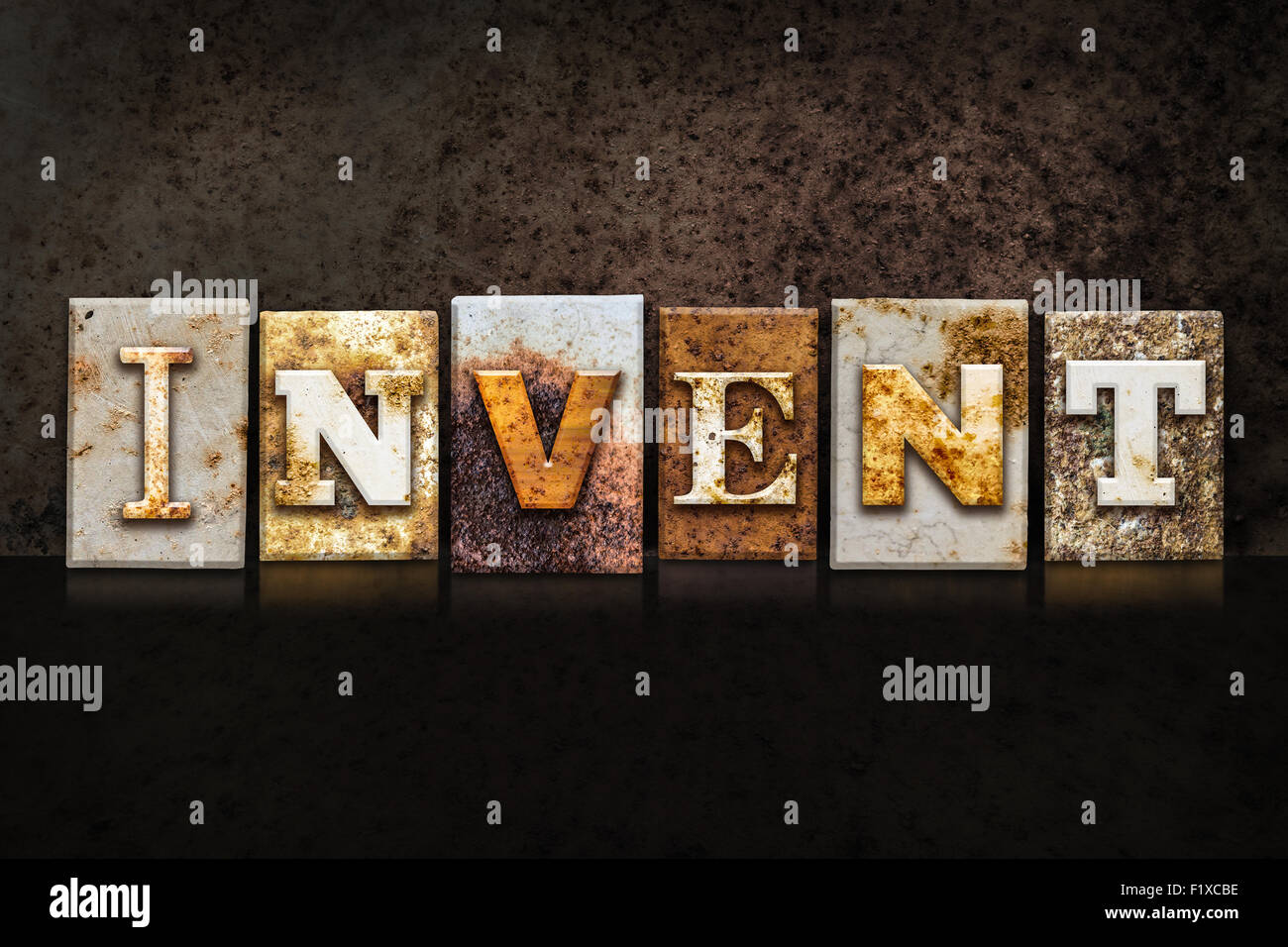 The word "INVENT" written in rusty metal letterpress type on a dark ...
