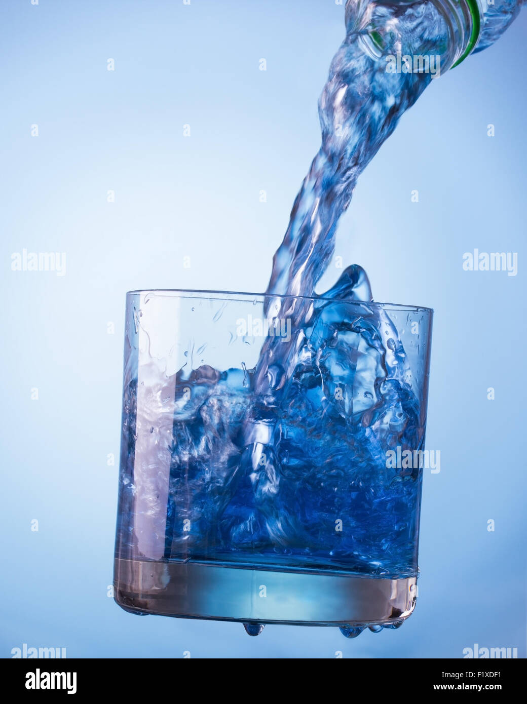 Pouring water into glass on blue background Stock Photo - Alamy