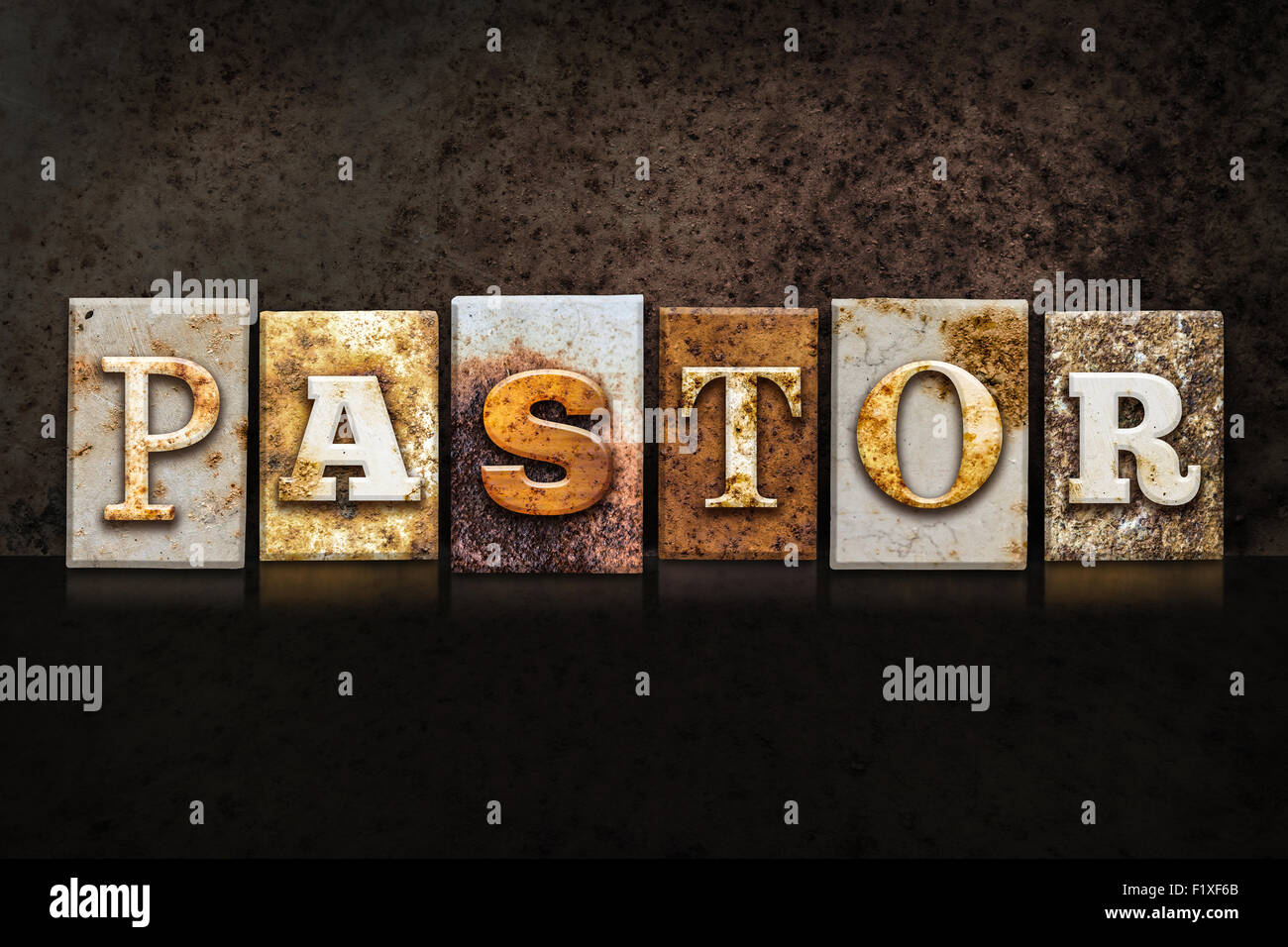 The word "PASTOR" written in rusty metal letterpress type on a dark ...