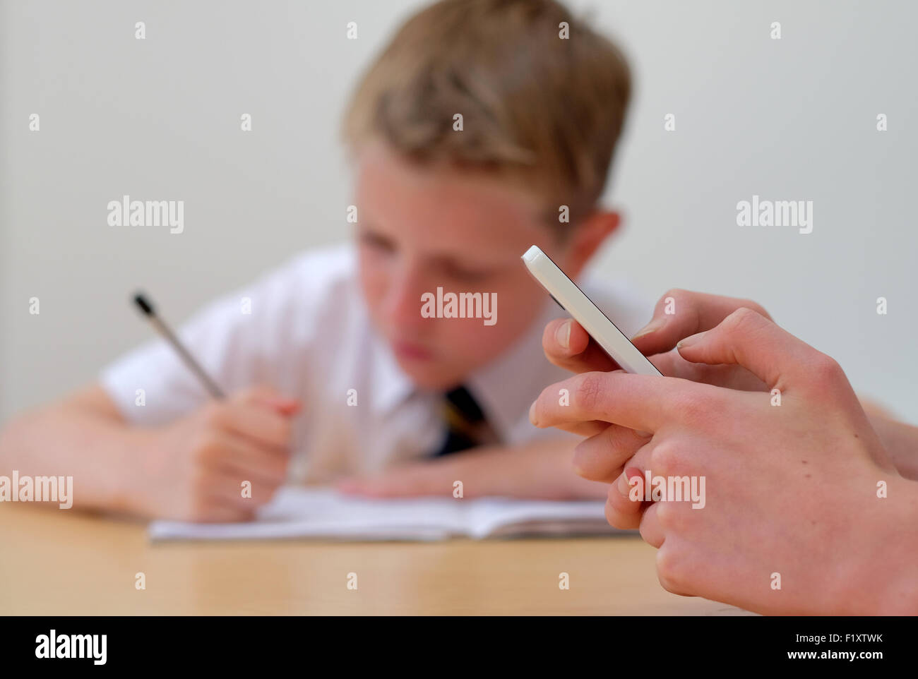 A school pupil using a mobile phone (texting) in class as another pupil ...